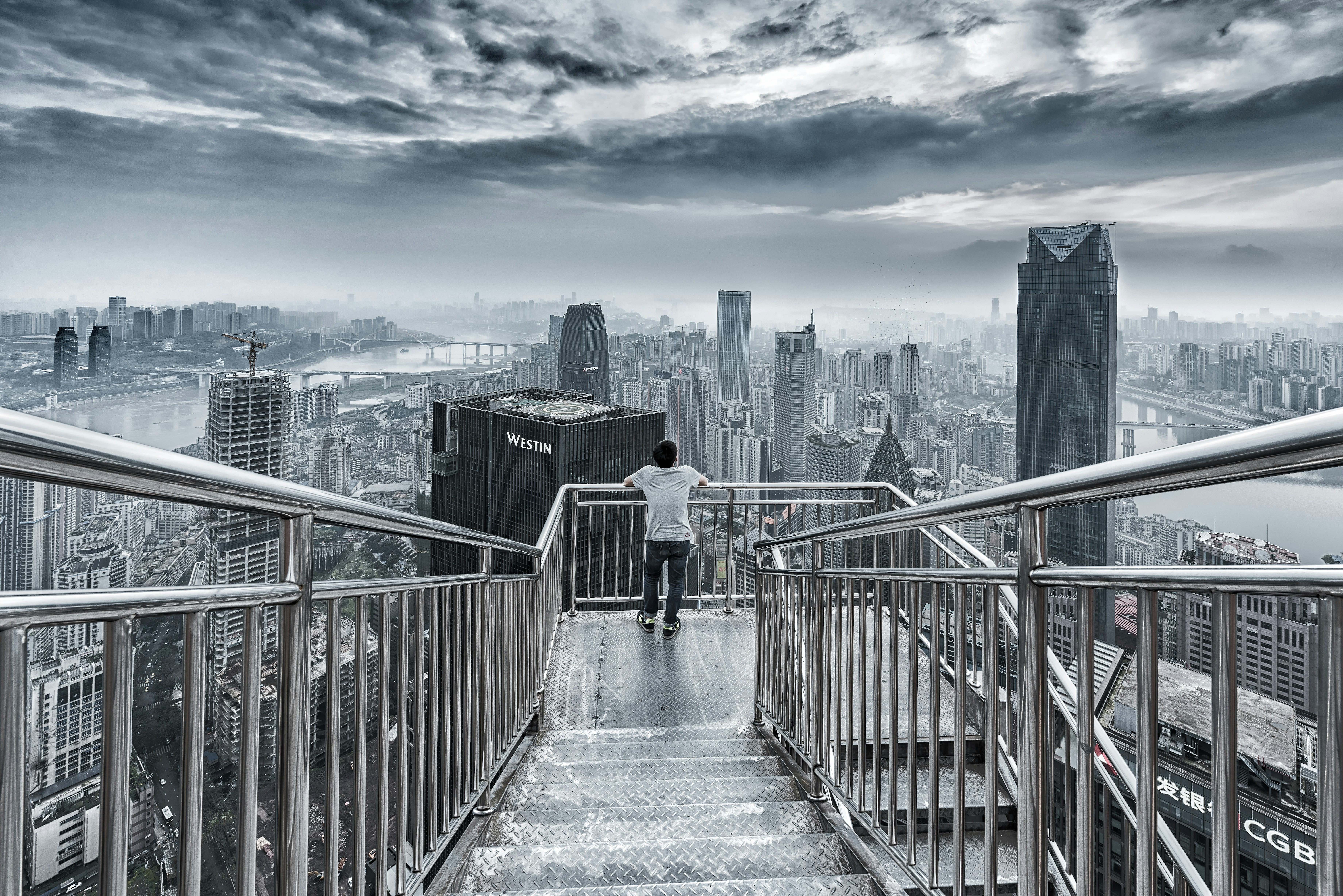 Man standing while hands resting on guard rail overlooking the city ...