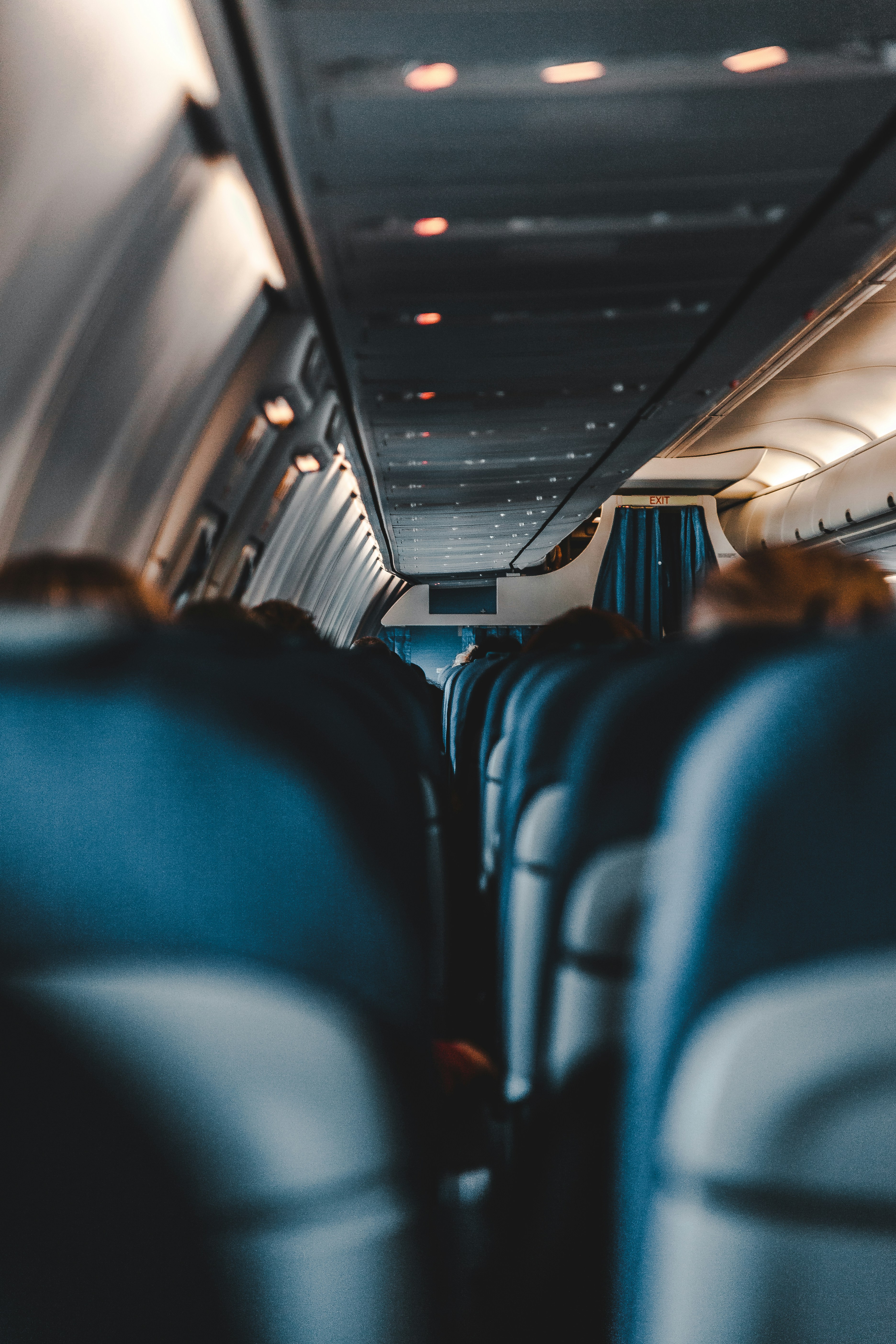 Interior view of an airplane cabin, showcasing rows of blue seats and soft overhead lighting. The perspective draws the viewer into the travel experience.