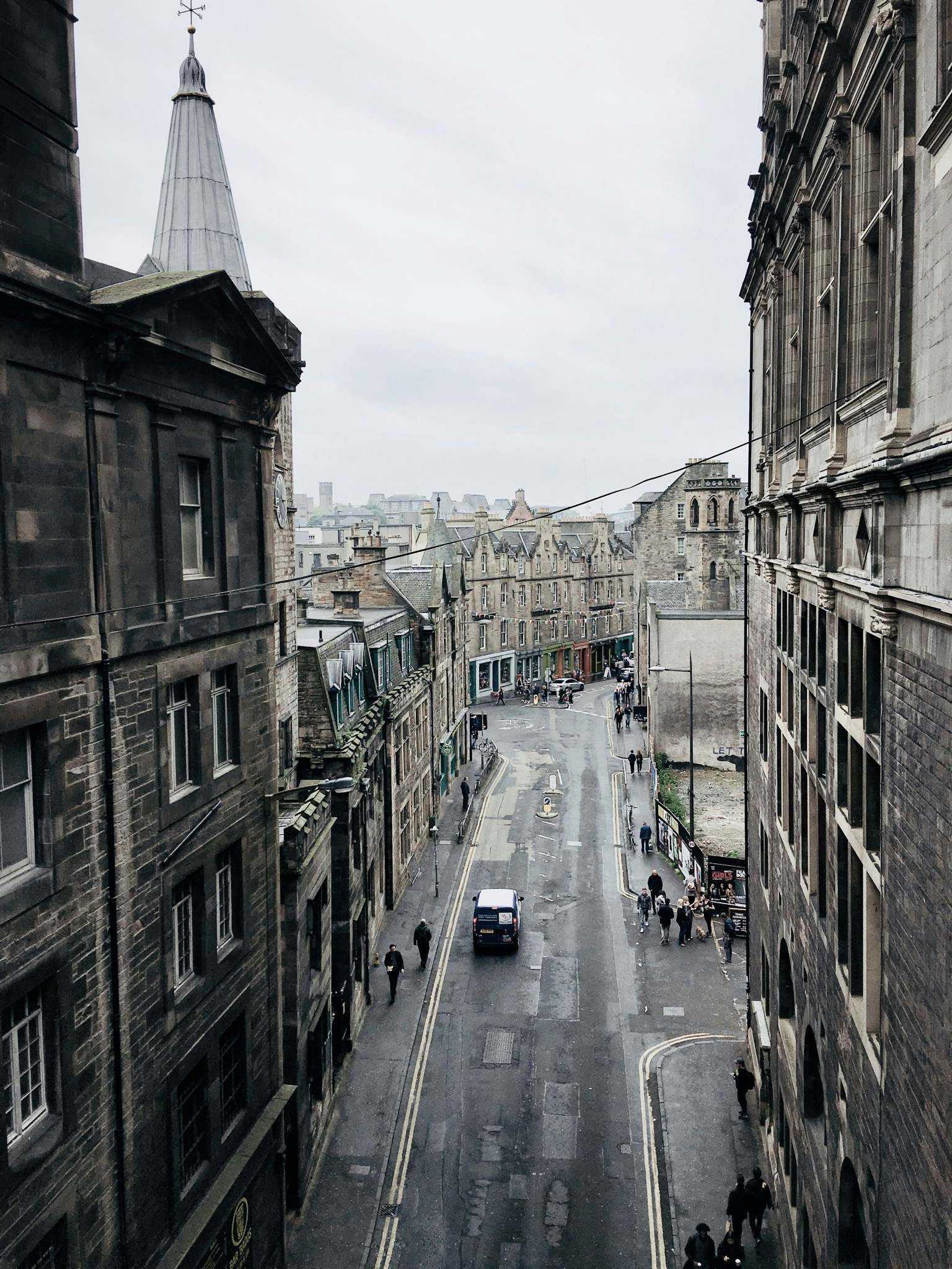 View of a cobblestone street lined with historic buildings in Edinburgh, showcasing a blend of architecture and urban life.