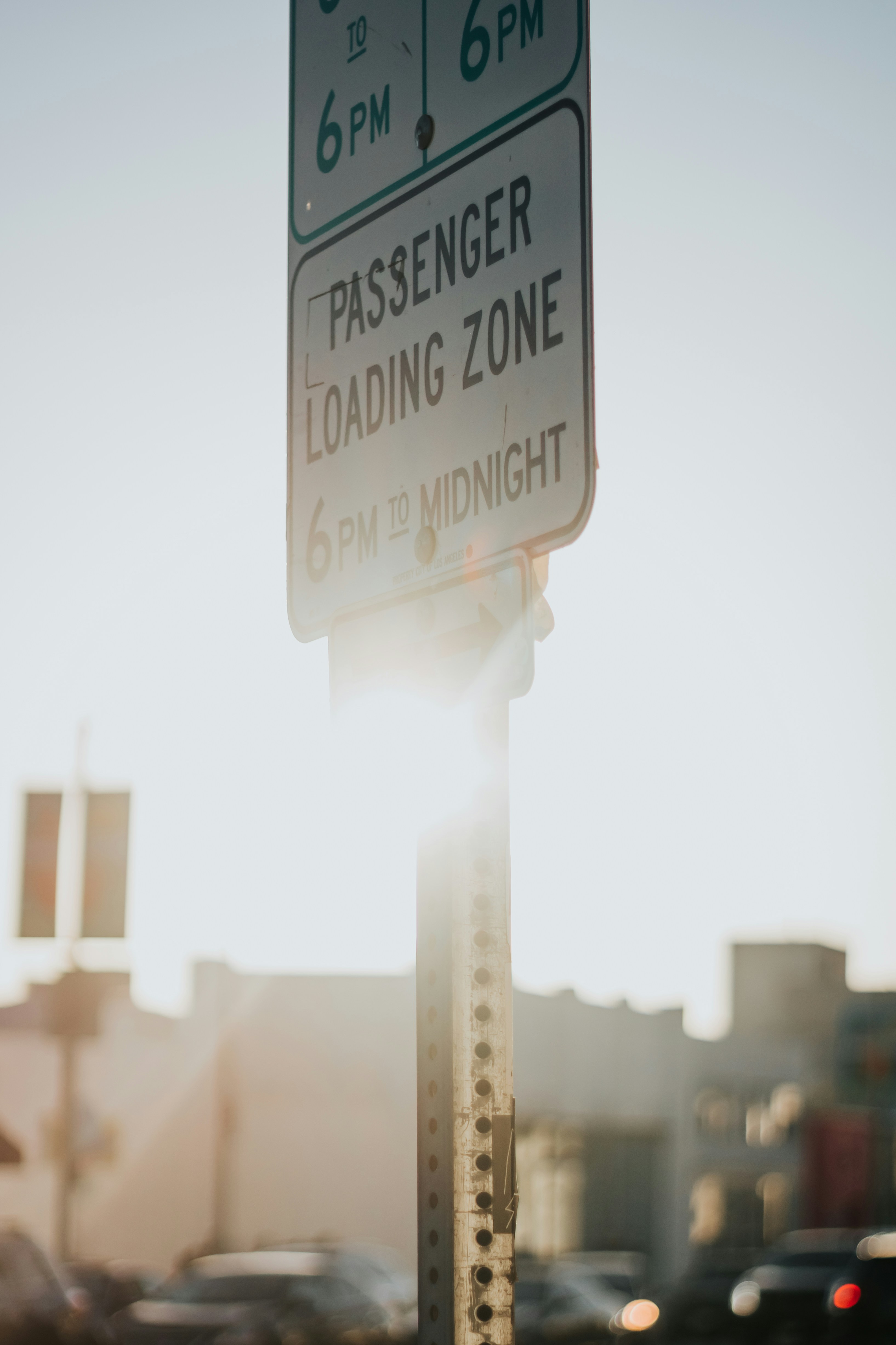 Passenger loading zone sign illuminated by the setting sun, casting a warm glow against a blurred urban backdrop.