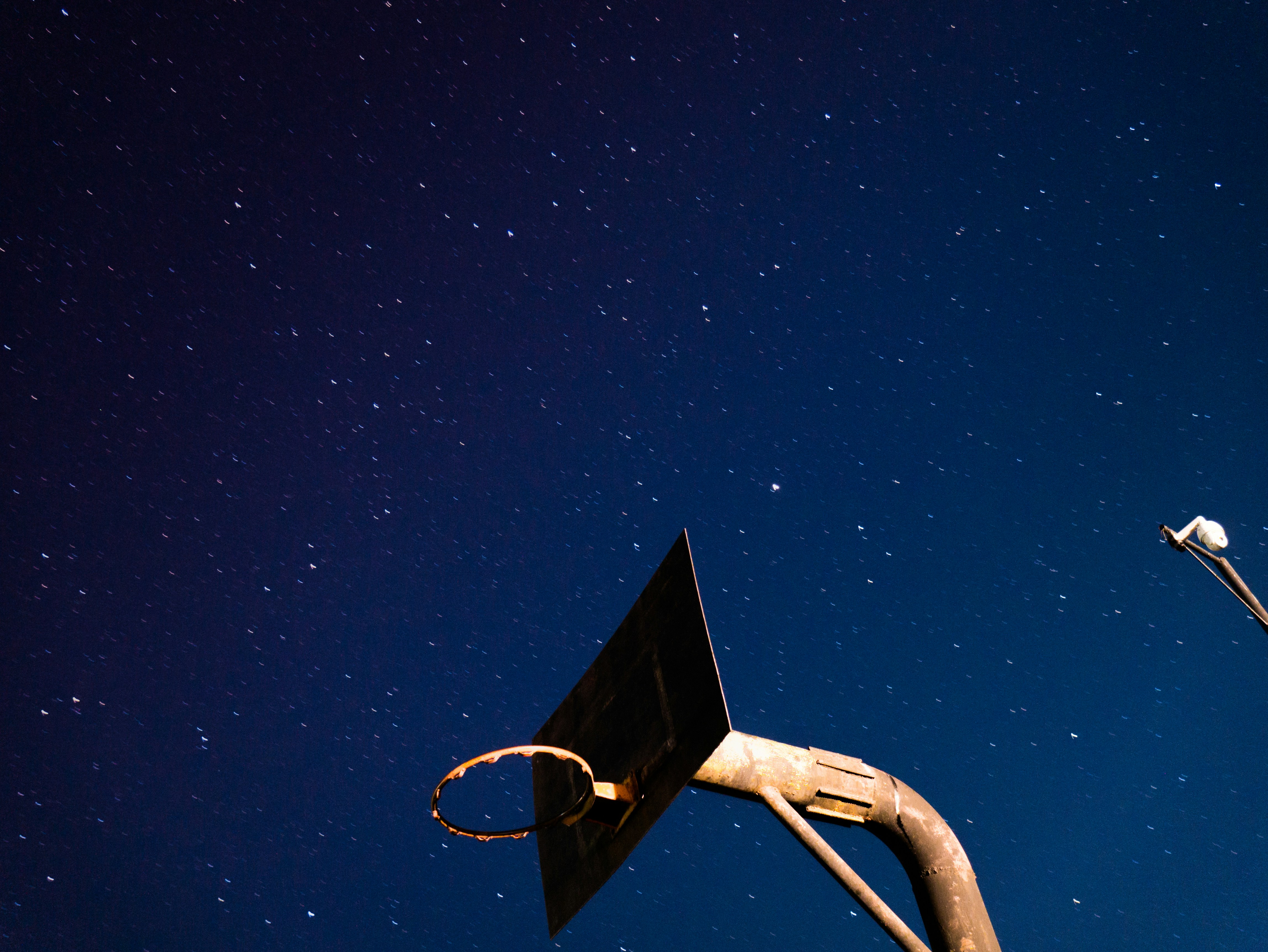 Weathered basketball hoop silhouetted against a starry night sky, evoking a sense of nostalgia and tranquility.