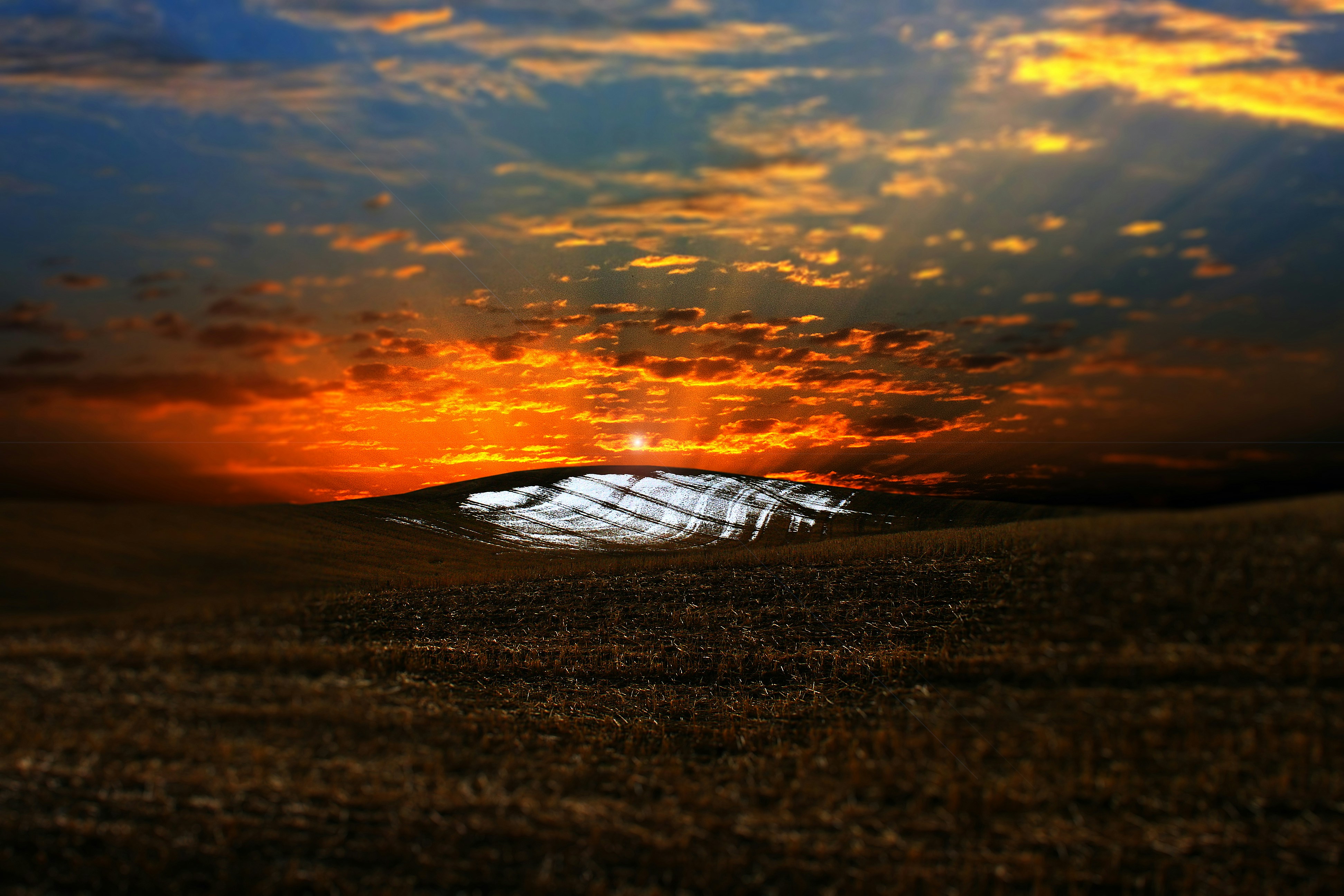Sunset over rolling fields with a dusting of snow under a vibrant orange sky.
