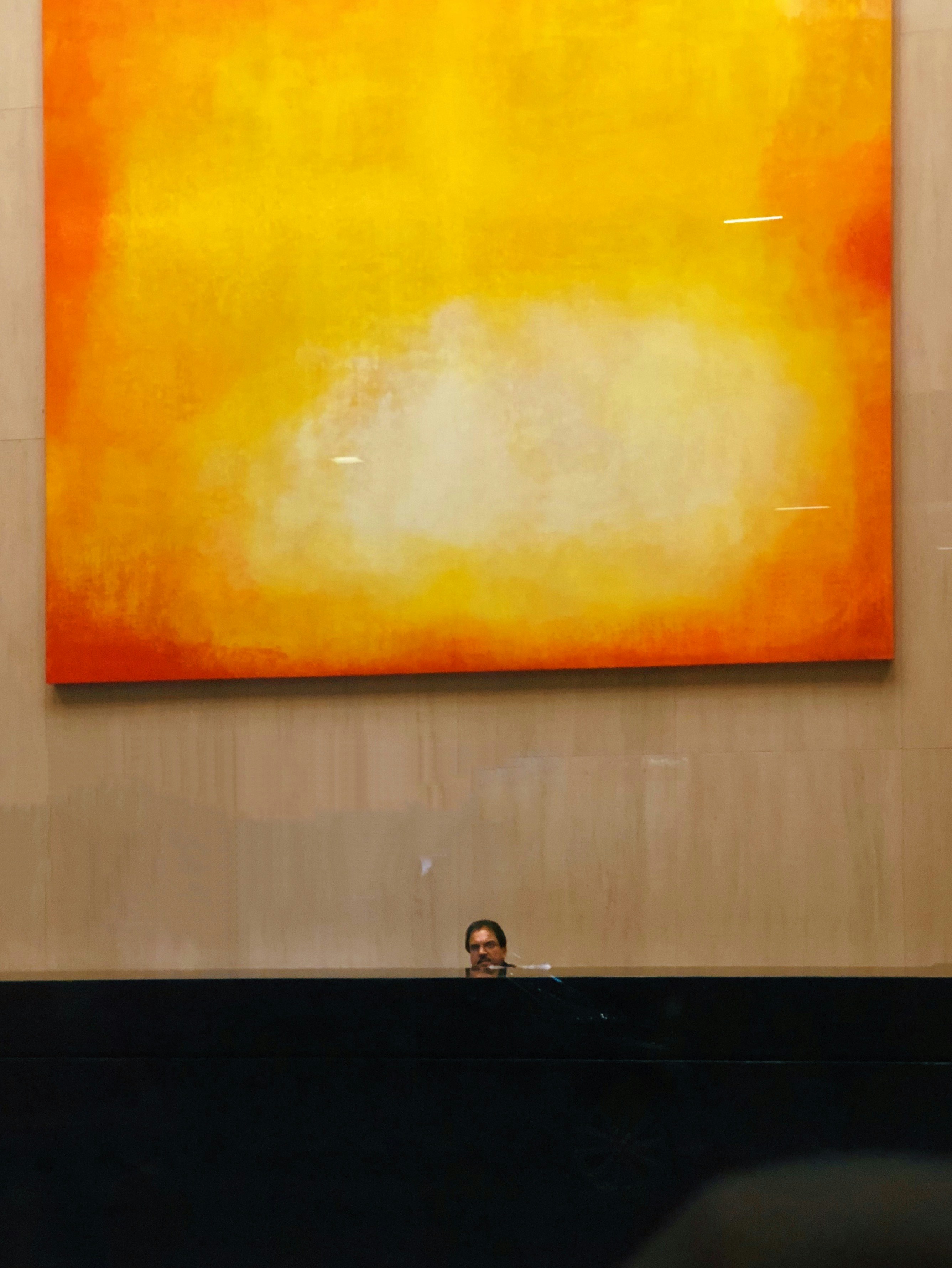 Vibrant abstract painting featuring hues of yellow and orange, with a figure partially visible below, creating a contrast between art and observer.