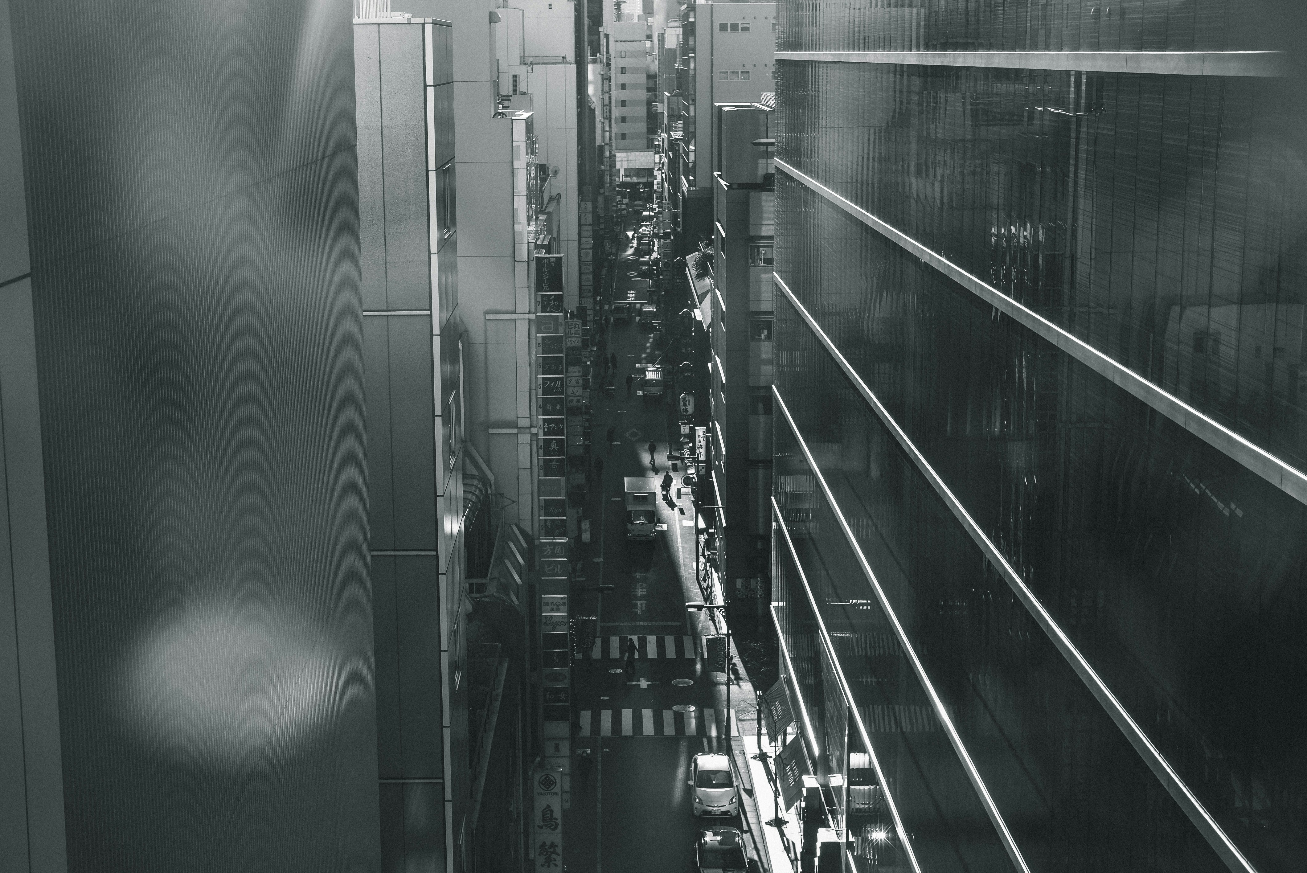 Narrow city street flanked by towering buildings with sunlight casting dramatic shadows.