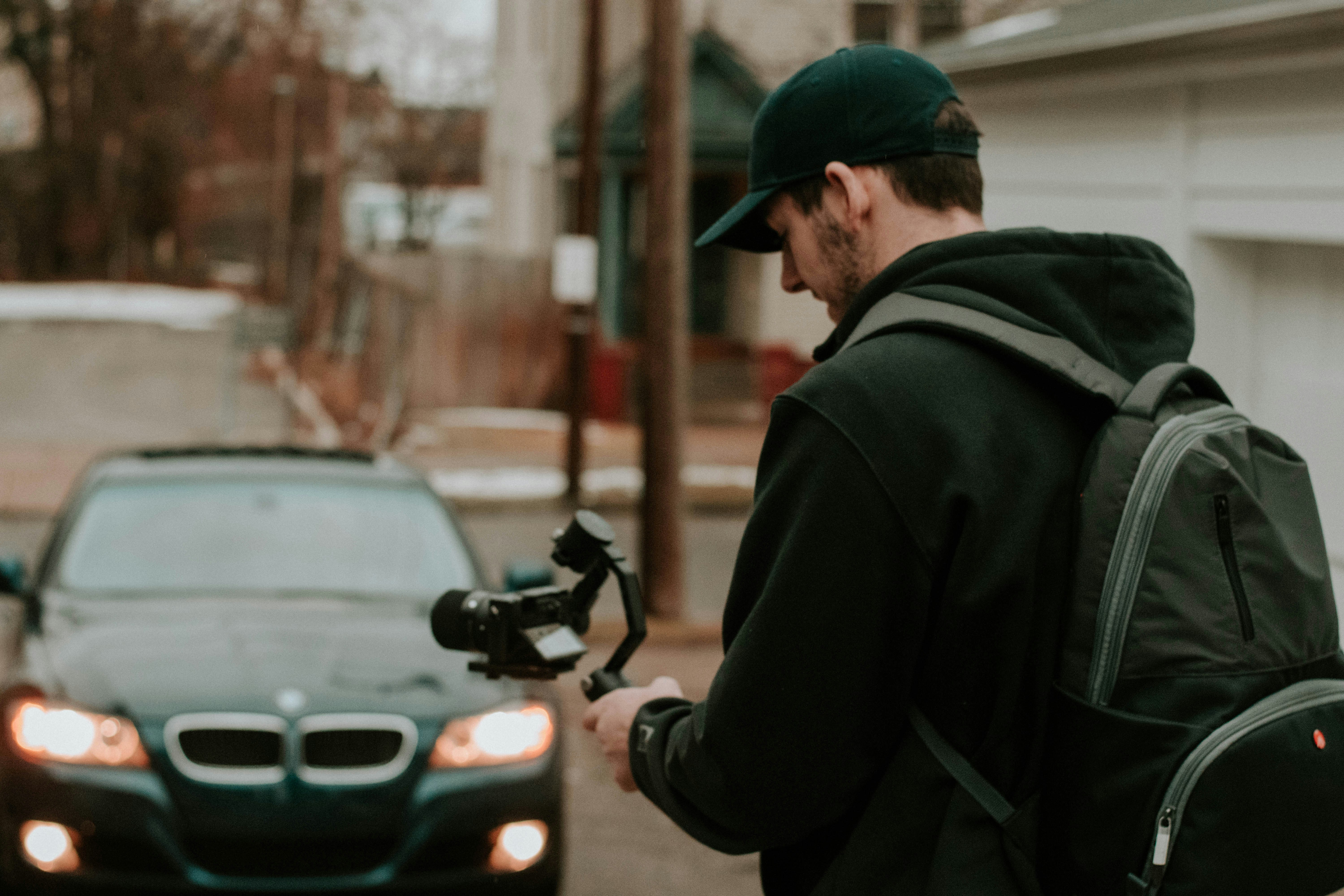 Gimbal Check on a Quiet Street: a backpacked photographer calibrates a handheld rig beside a waiting car