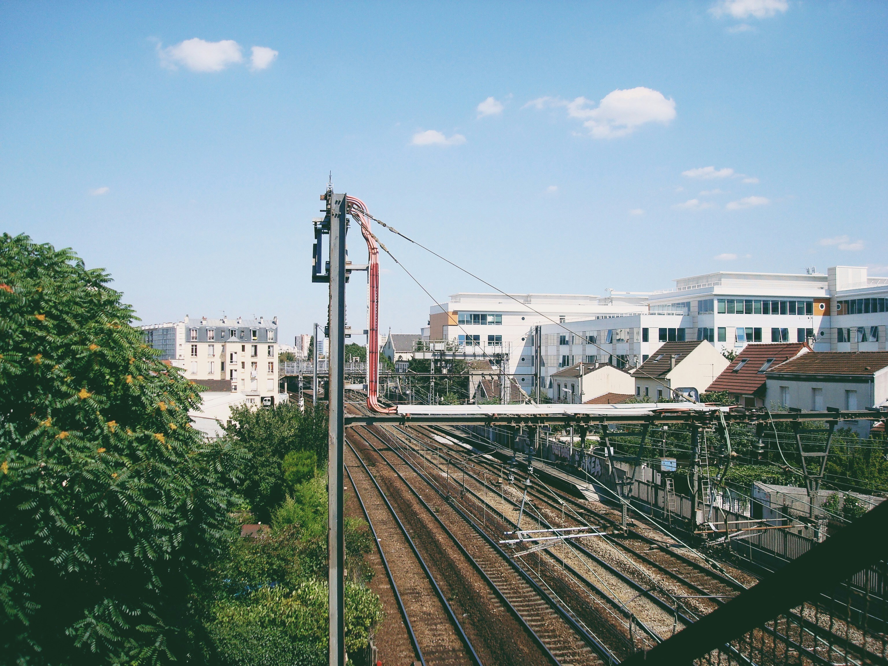Railway tracks stretching through a residential area with a clear blue sky and scattered clouds.