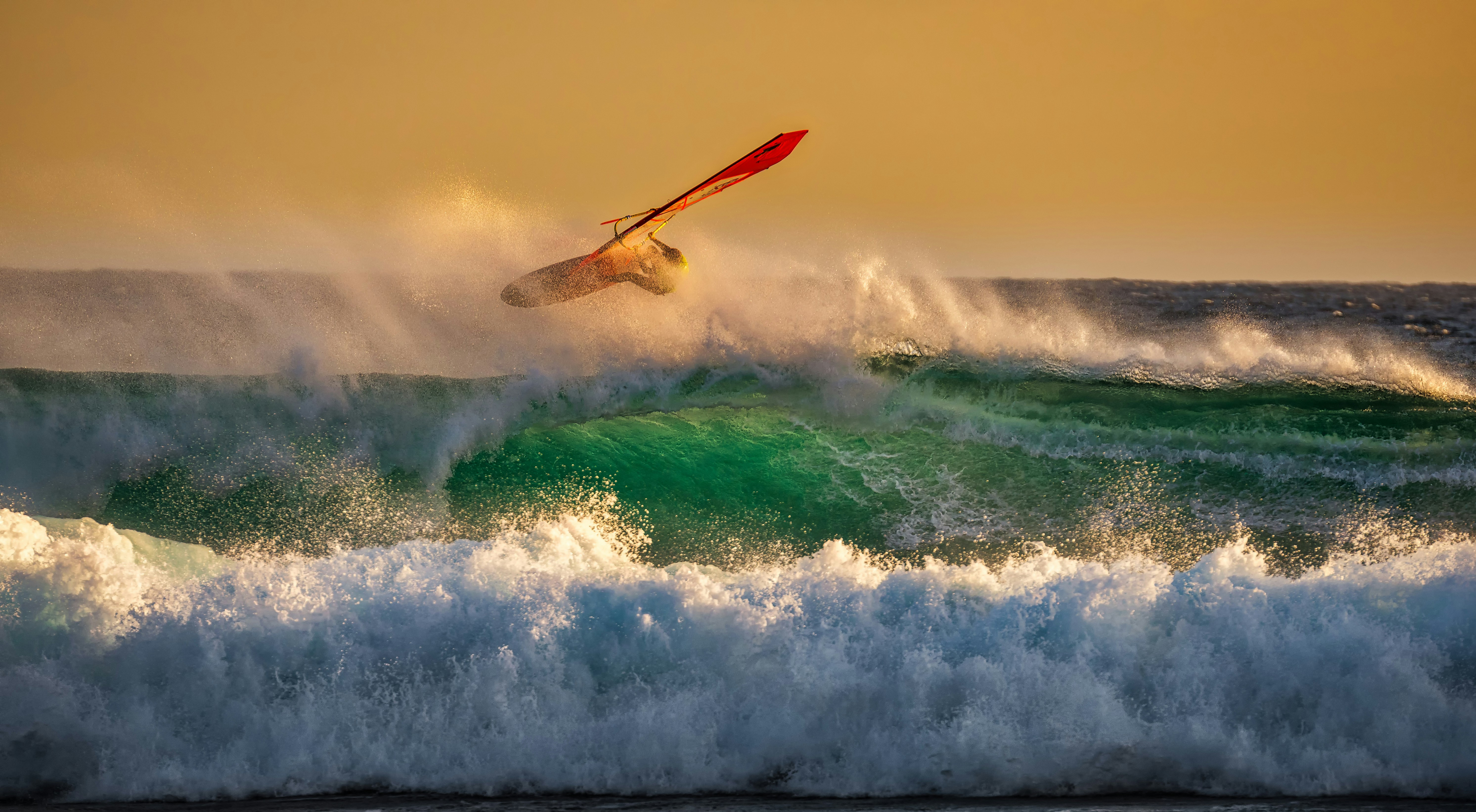 Flight over green crest: a surfer sprints above a curling wave at sunset