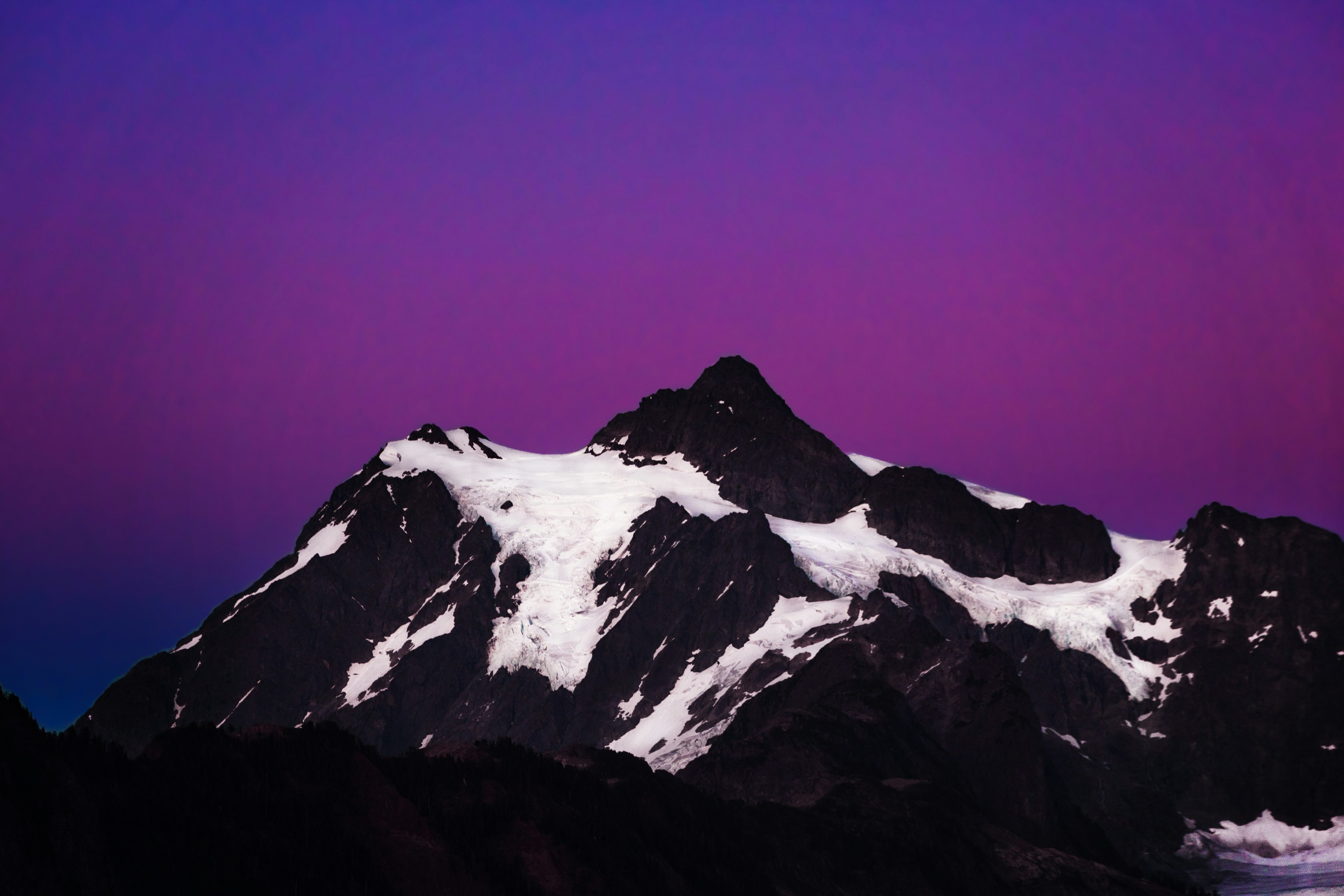 Majestic mountain range under a gradient twilight sky, highlighting the contrast of snow and rock formations.