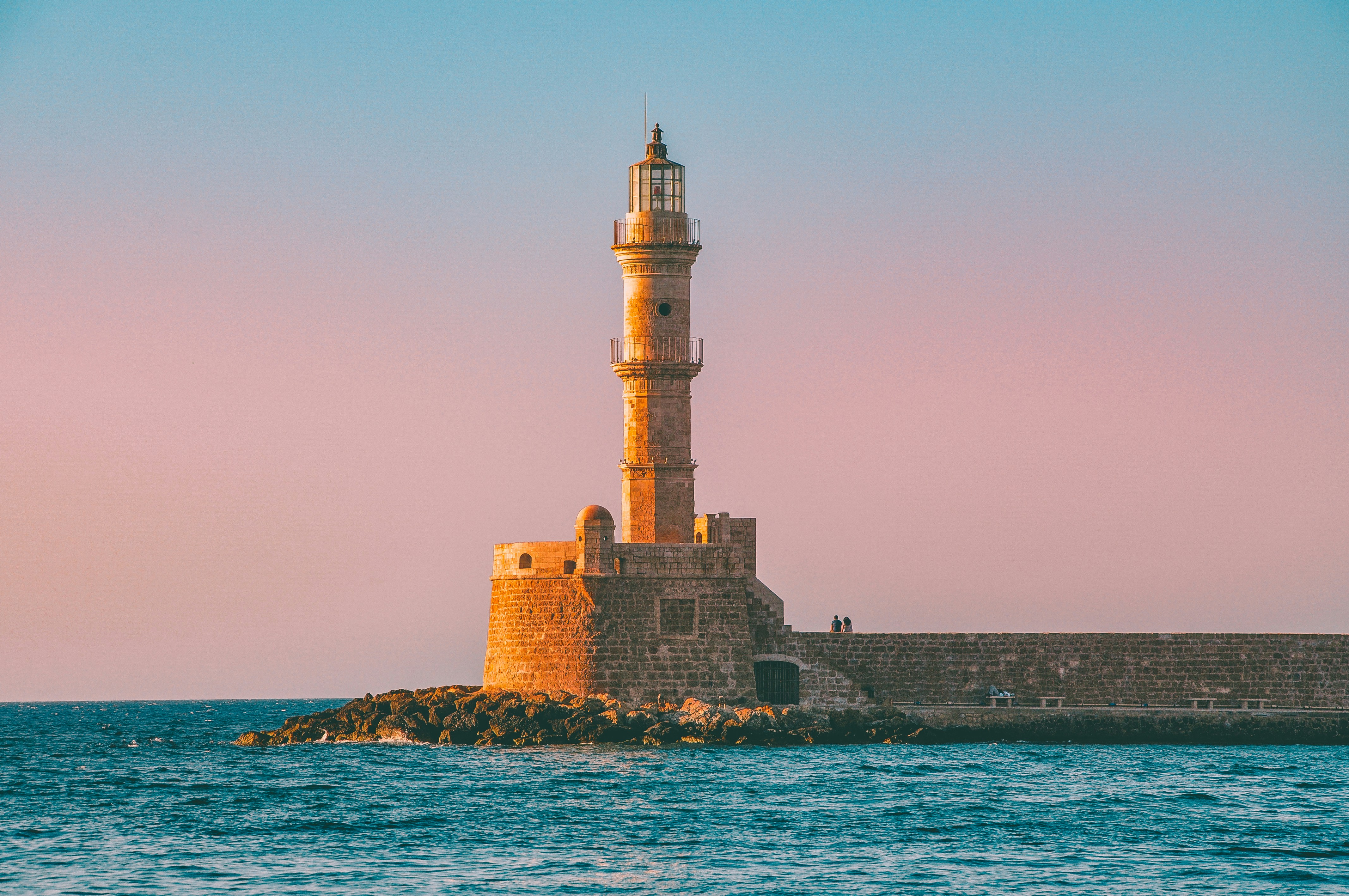 A historic lighthouse stands proudly on a rocky outcrop, overlooking the tranquil sea during twilight. The soft hues of the sky create a serene backdrop.