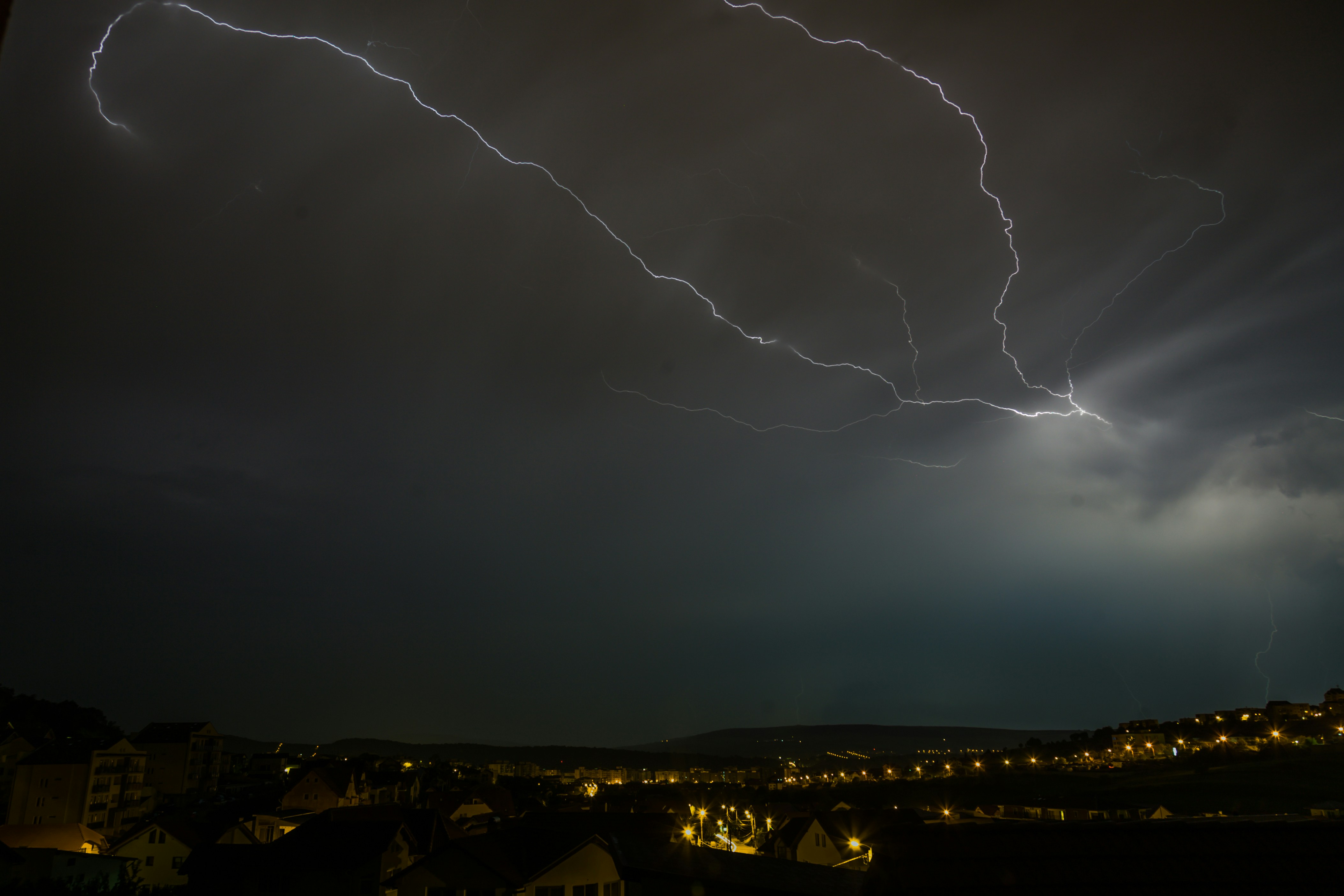 Lightning branches across a stormy night sky above a dimly lit town.