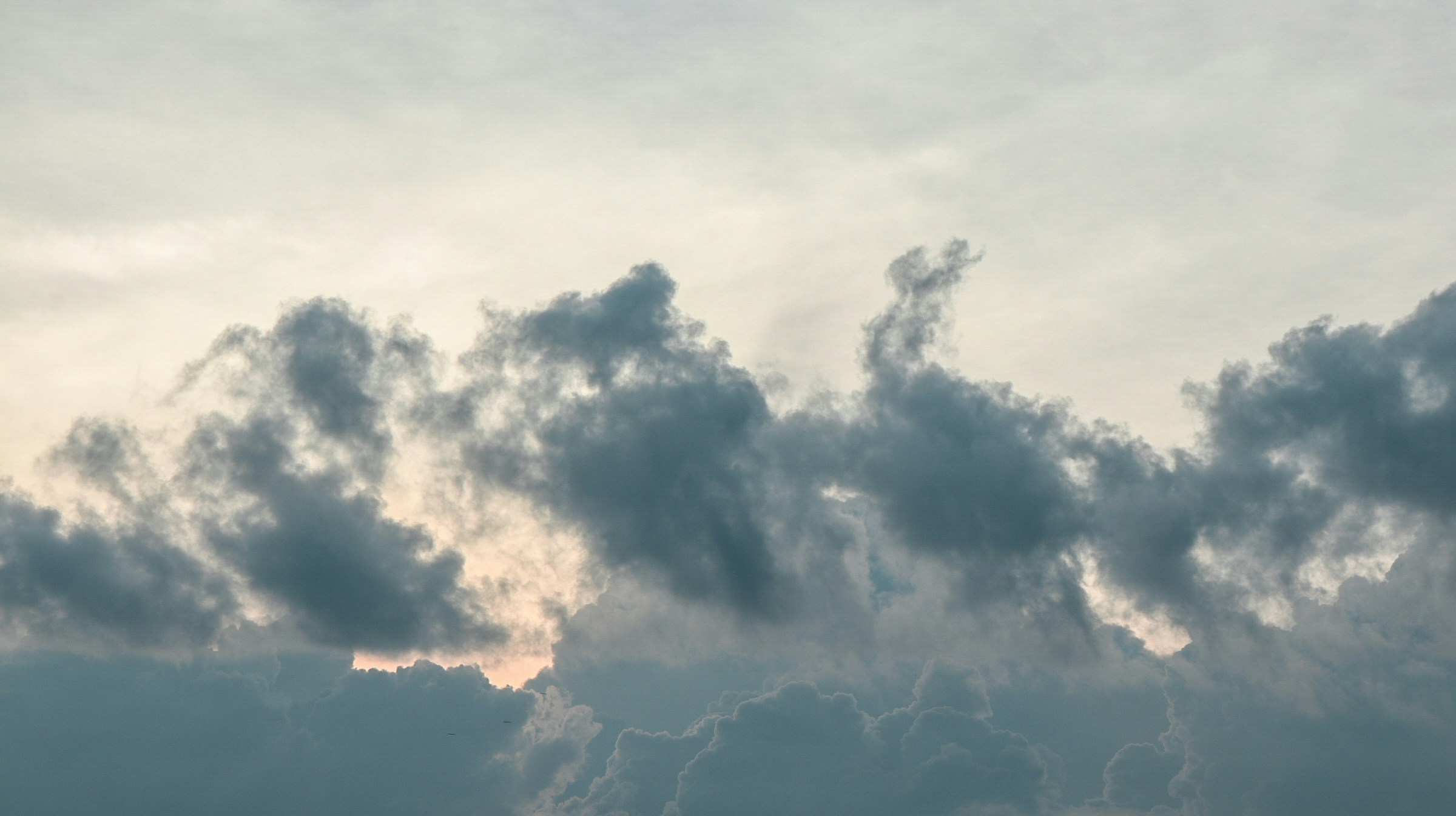 This photograph shows soft, layered clouds drifting across a pale sky with a subtle sun glow along the horizon. The scene emphasizes cloud texture and atmospheric light.