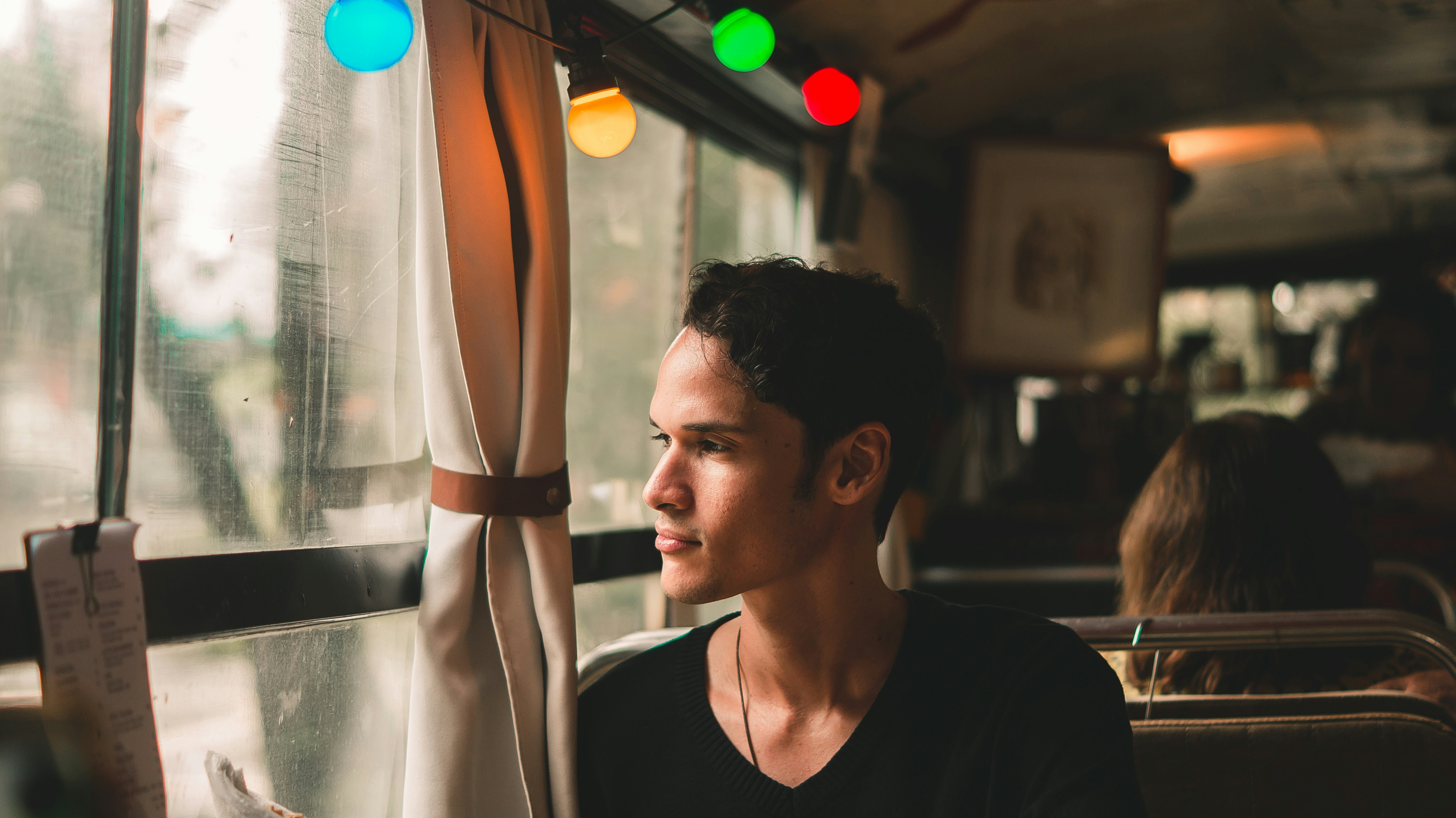 Man gazing out a bus window adorned with colorful lights.