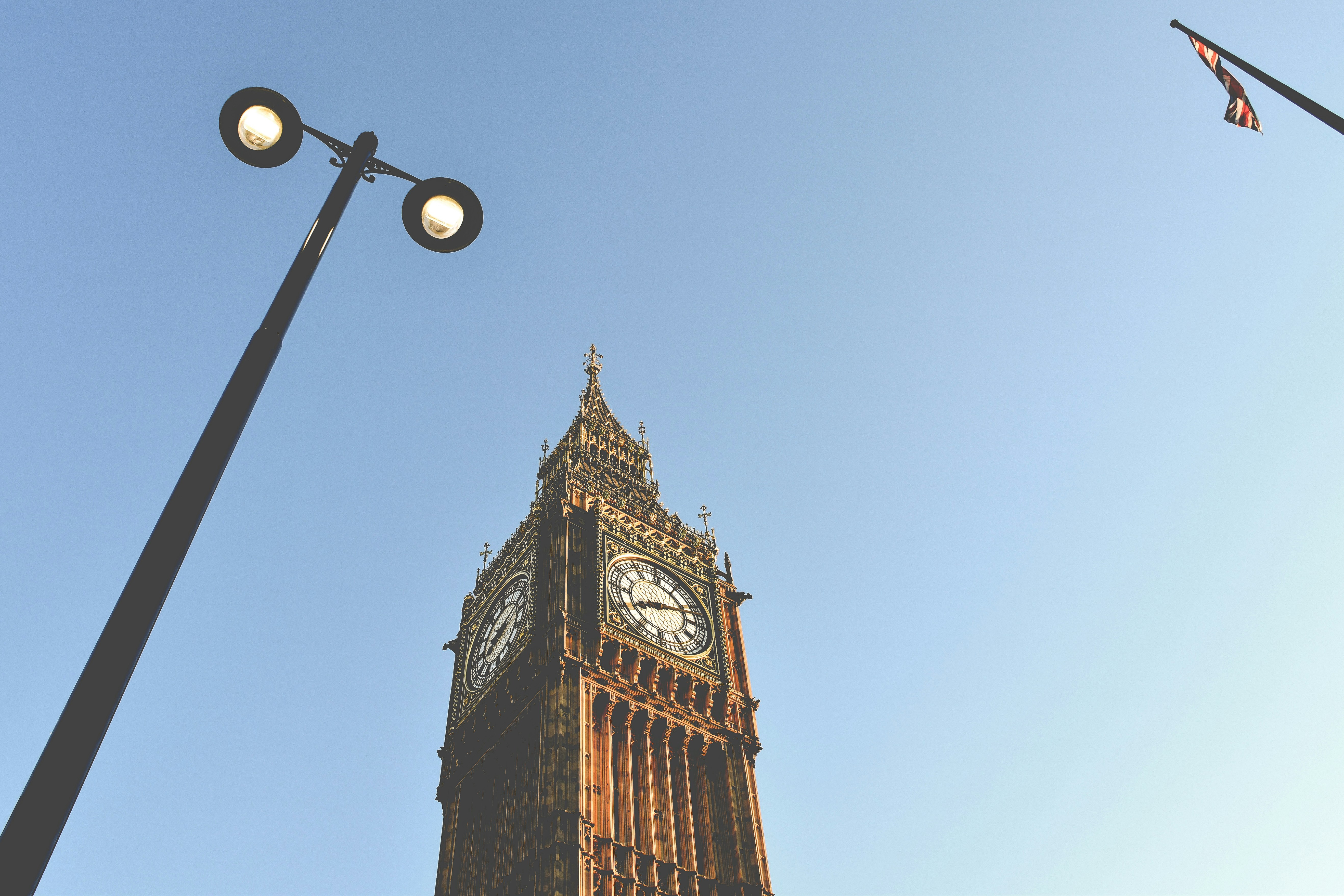 Iconic clock tower rises majestically against a clear sky, flanked by a street lamp and a fluttering flag.
