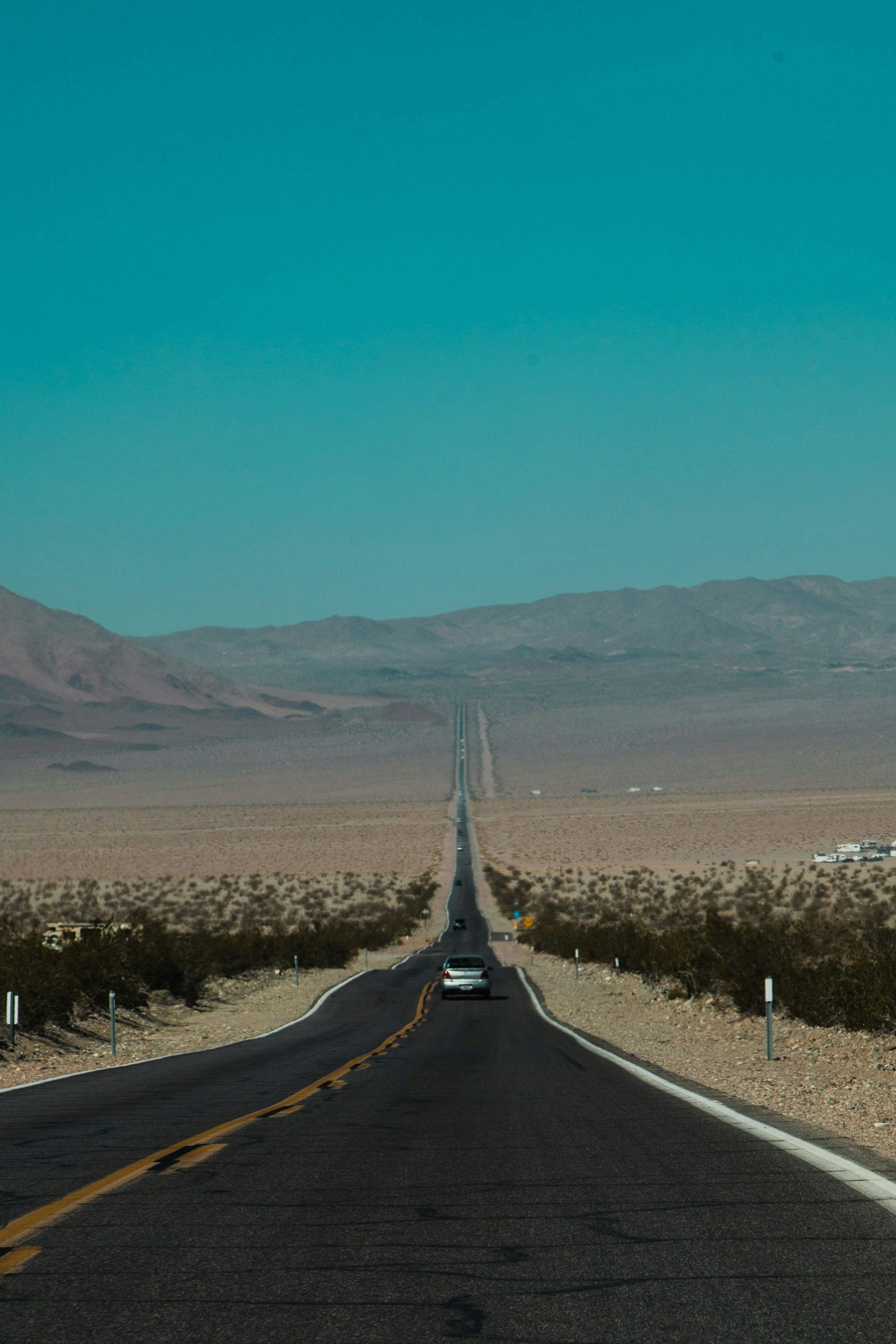 Lone Car on the Desert Spine: A Straight Road Toward the Distant Range