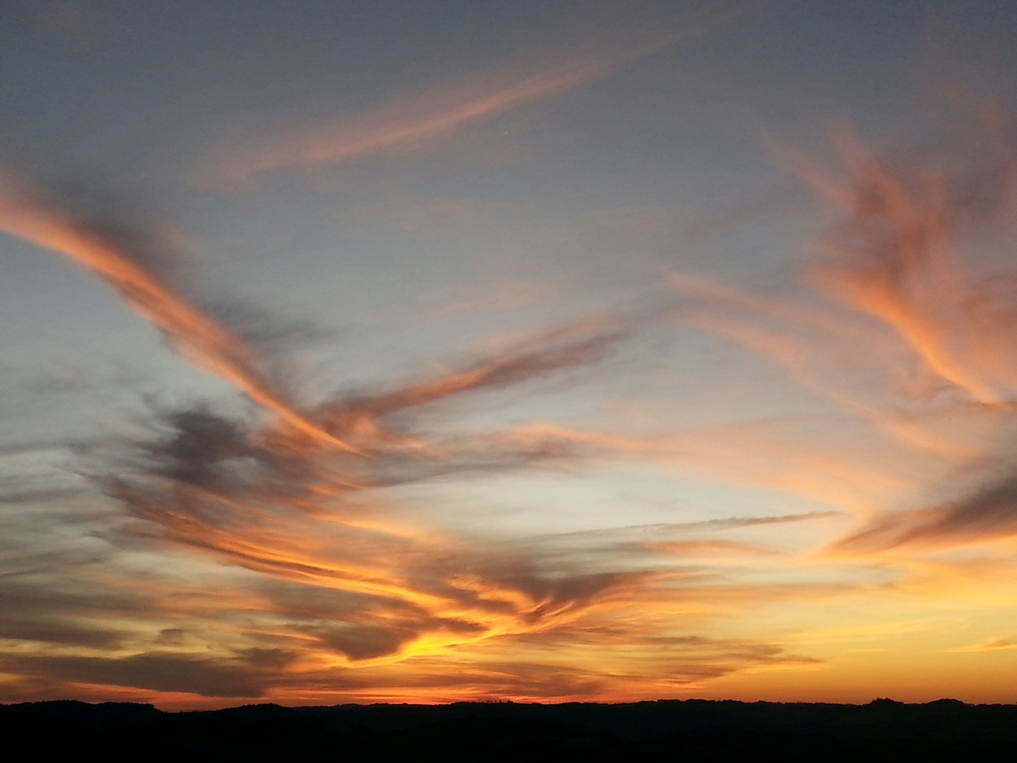 Vibrant orange and pink clouds swirl across a twilight sky above darkened hills.