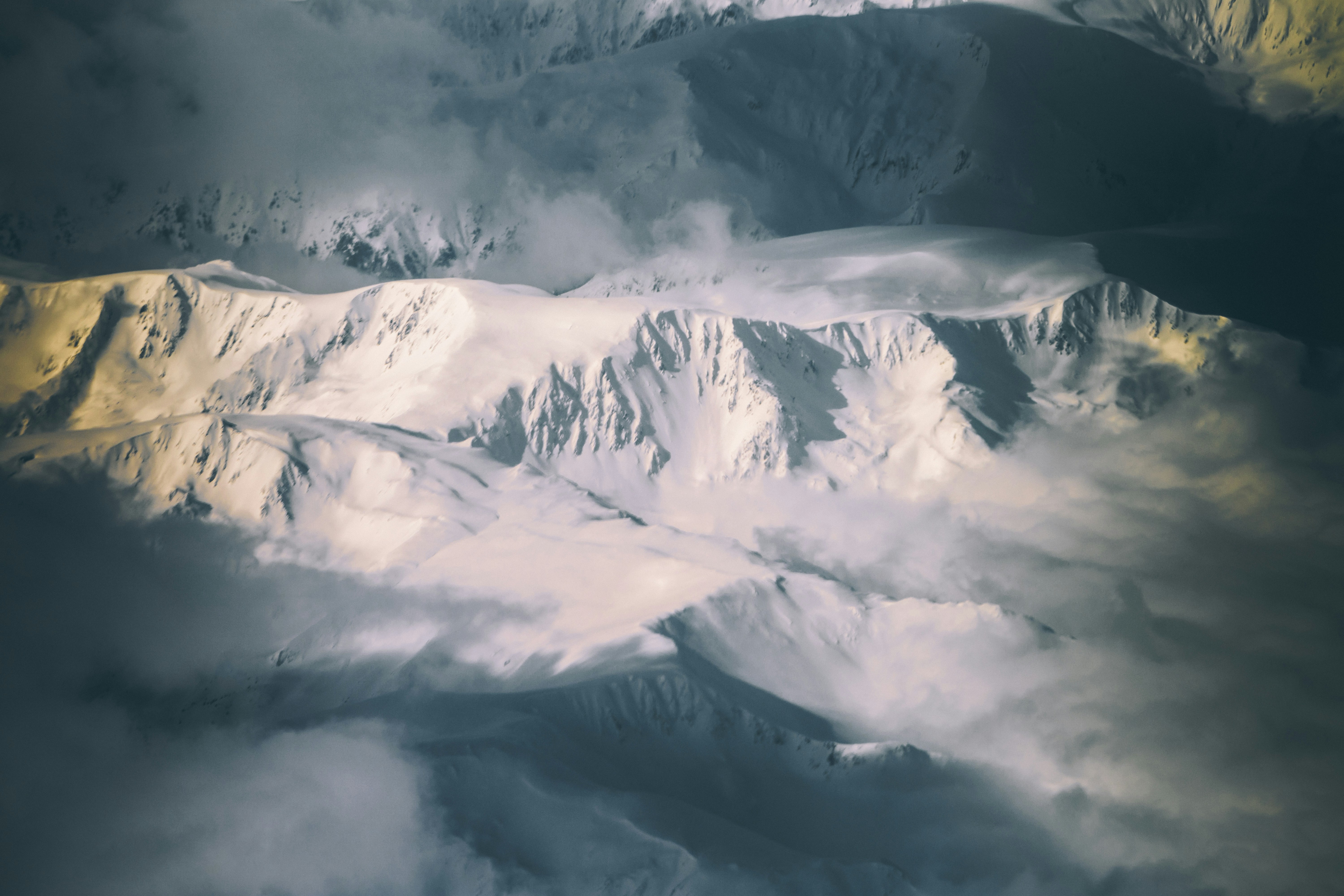 Sunlit Serrations: Snow-Crowned Peaks Beneath Veiled Clouds