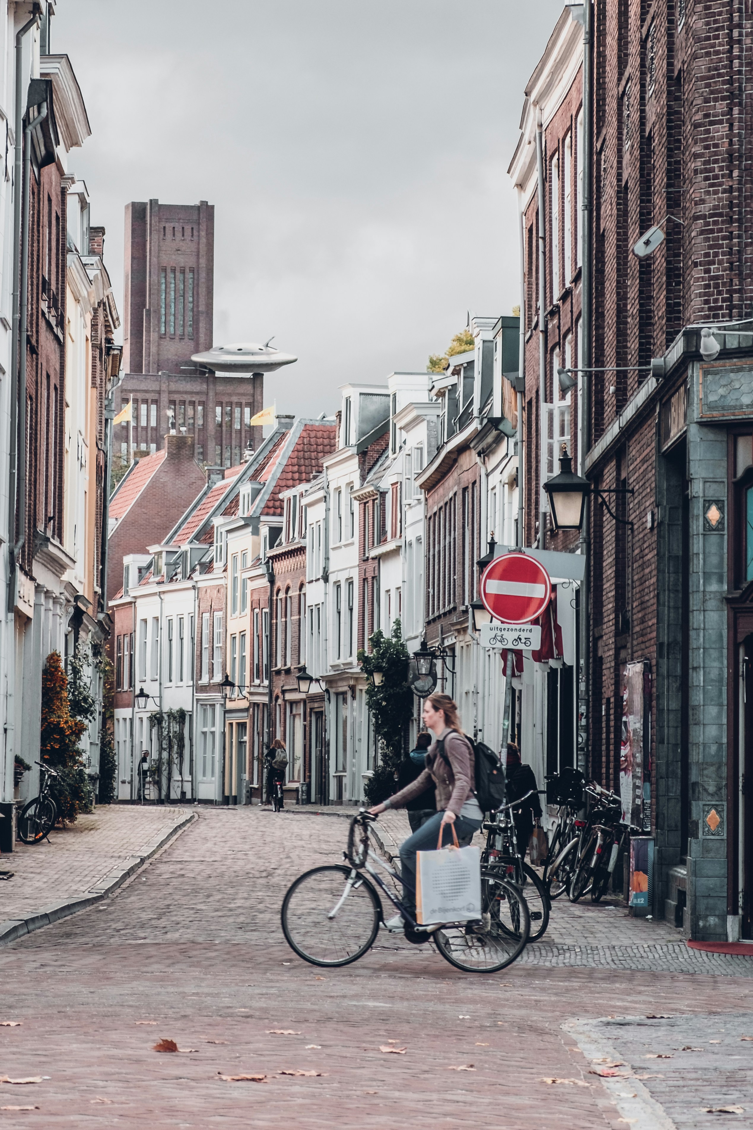 A cyclist navigates a narrow, cobblestone street lined with charming Dutch architecture and bicycles, capturing the essence of urban life.