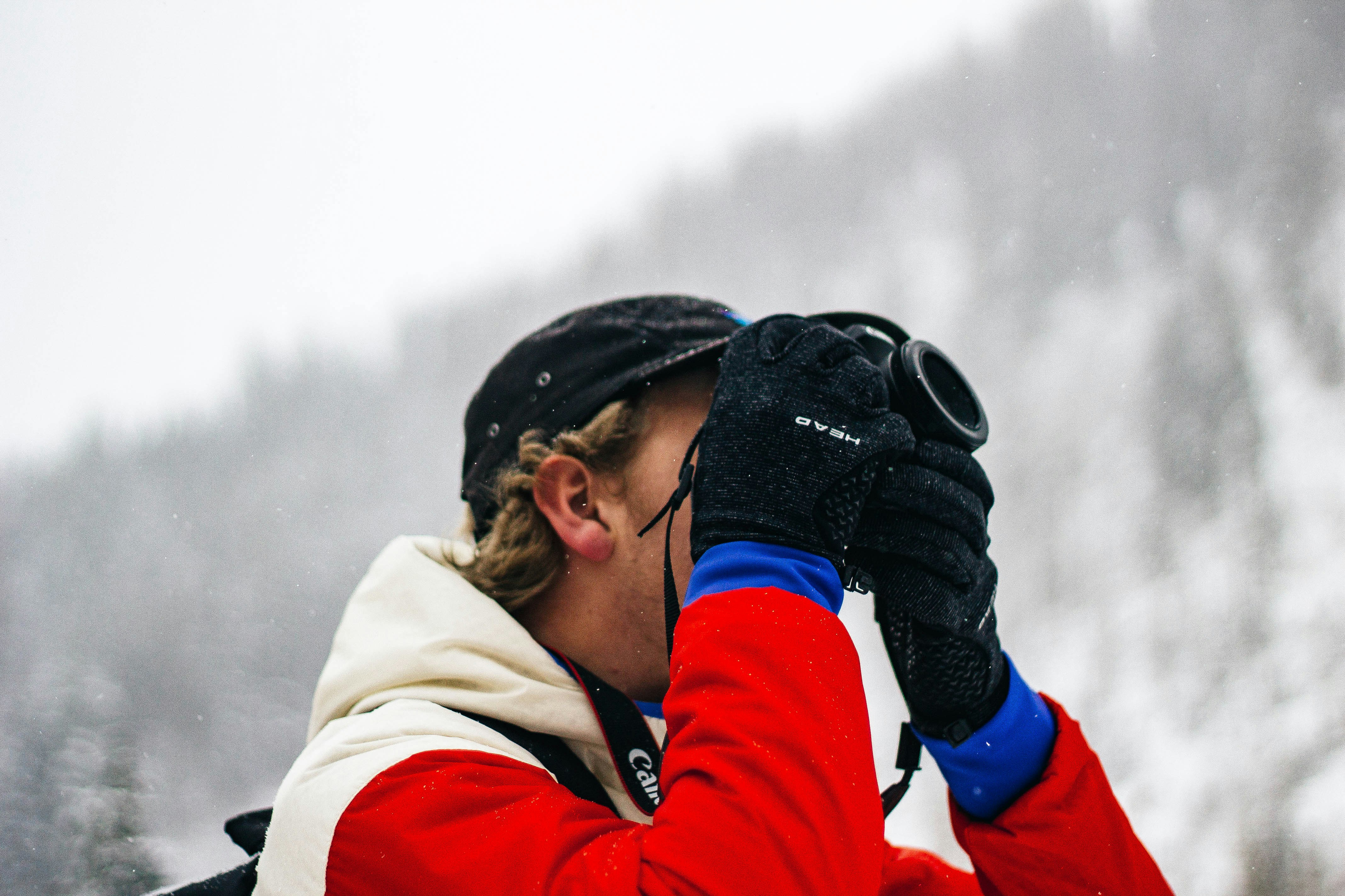 Person in red jacket photographing snowy landscape with dense trees.