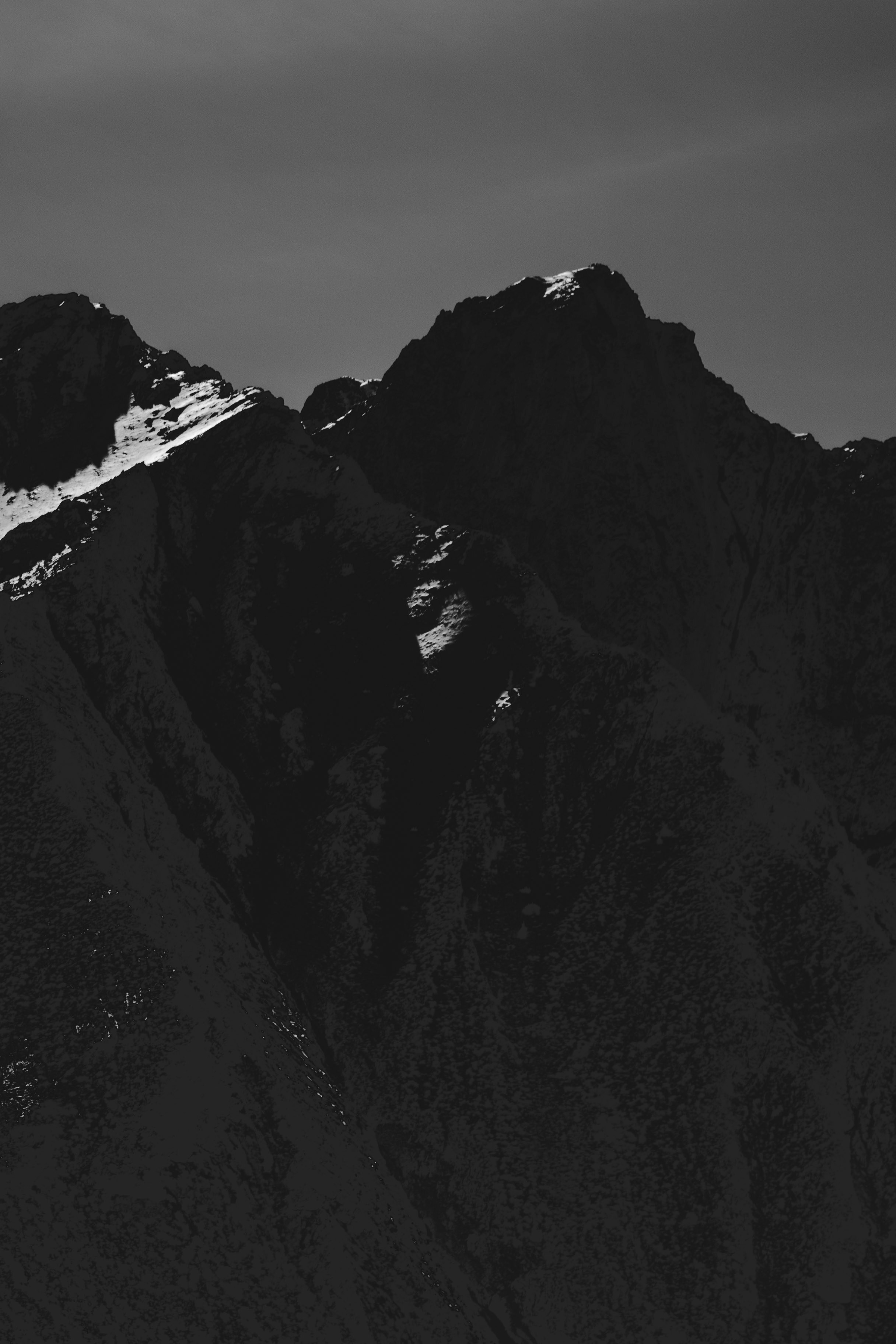 Dark mountain ridges contrasted by patches of snow under a dramatic sky.