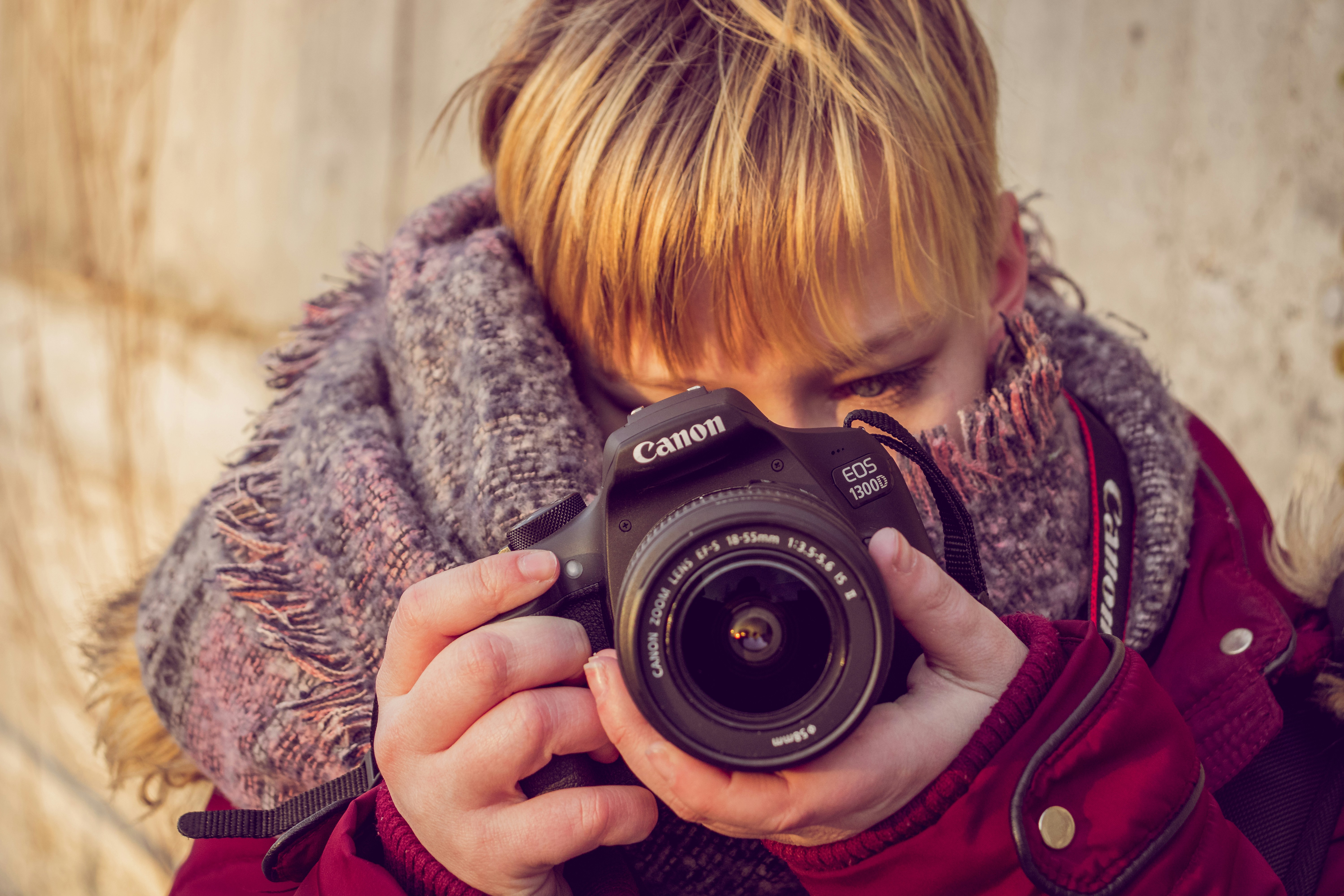 A young photographer in a cozy scarf focuses intently on capturing a moment with a Canon EOS 77D camera.