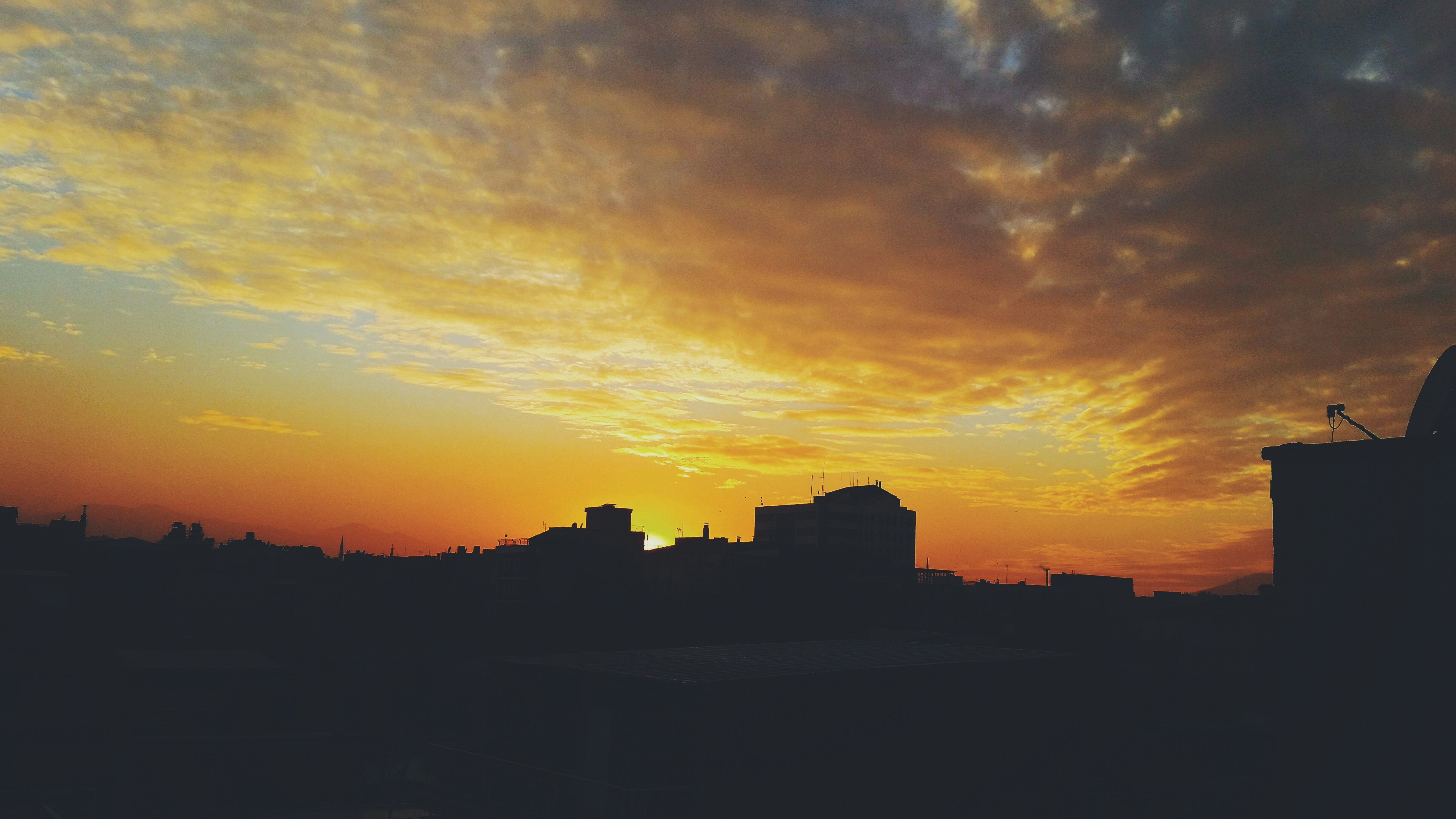 Silhouette of city buildings against a vibrant sunrise with dramatic clouds.