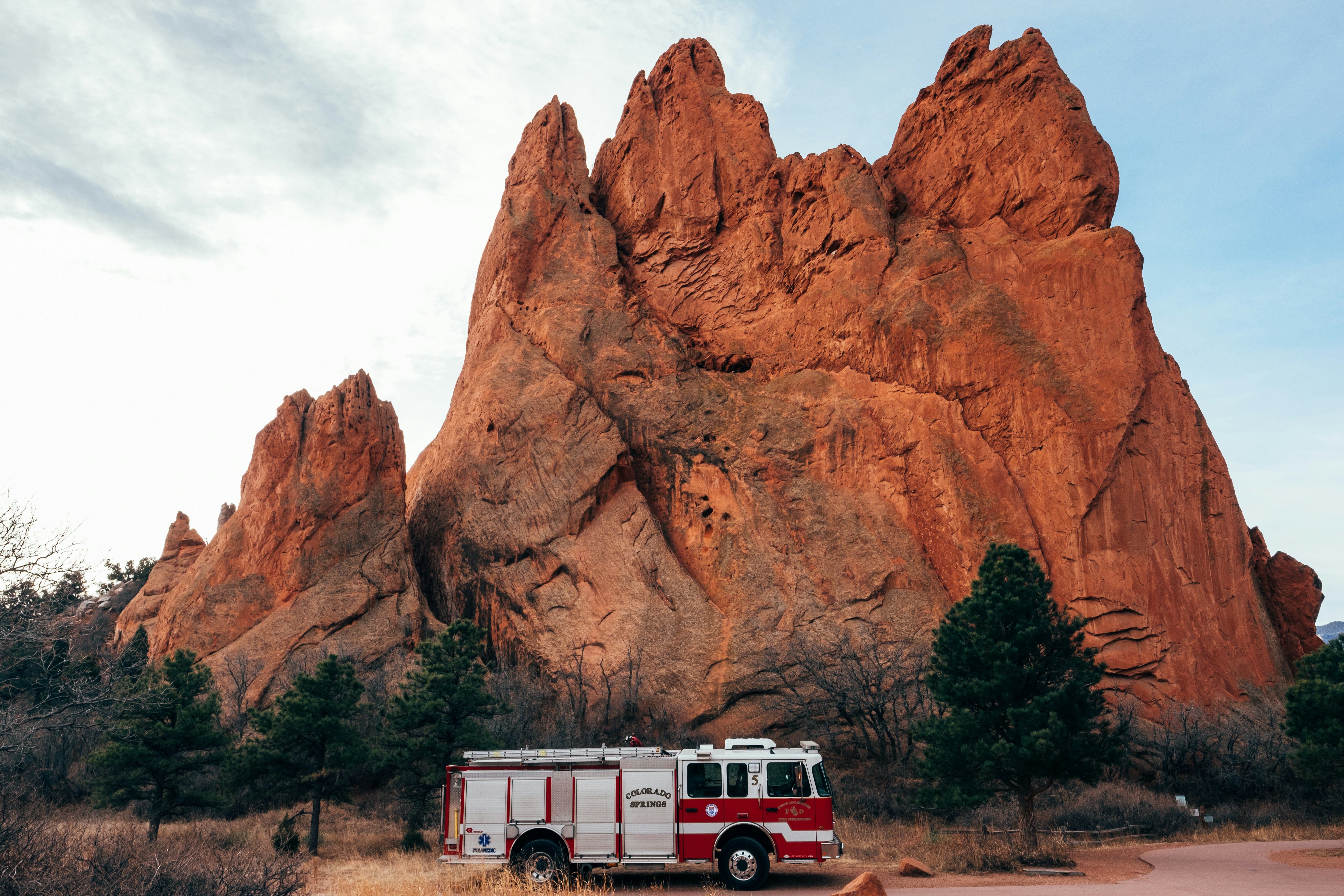 Fire truck parked in front of towering red rock formations against a cloudy sky.