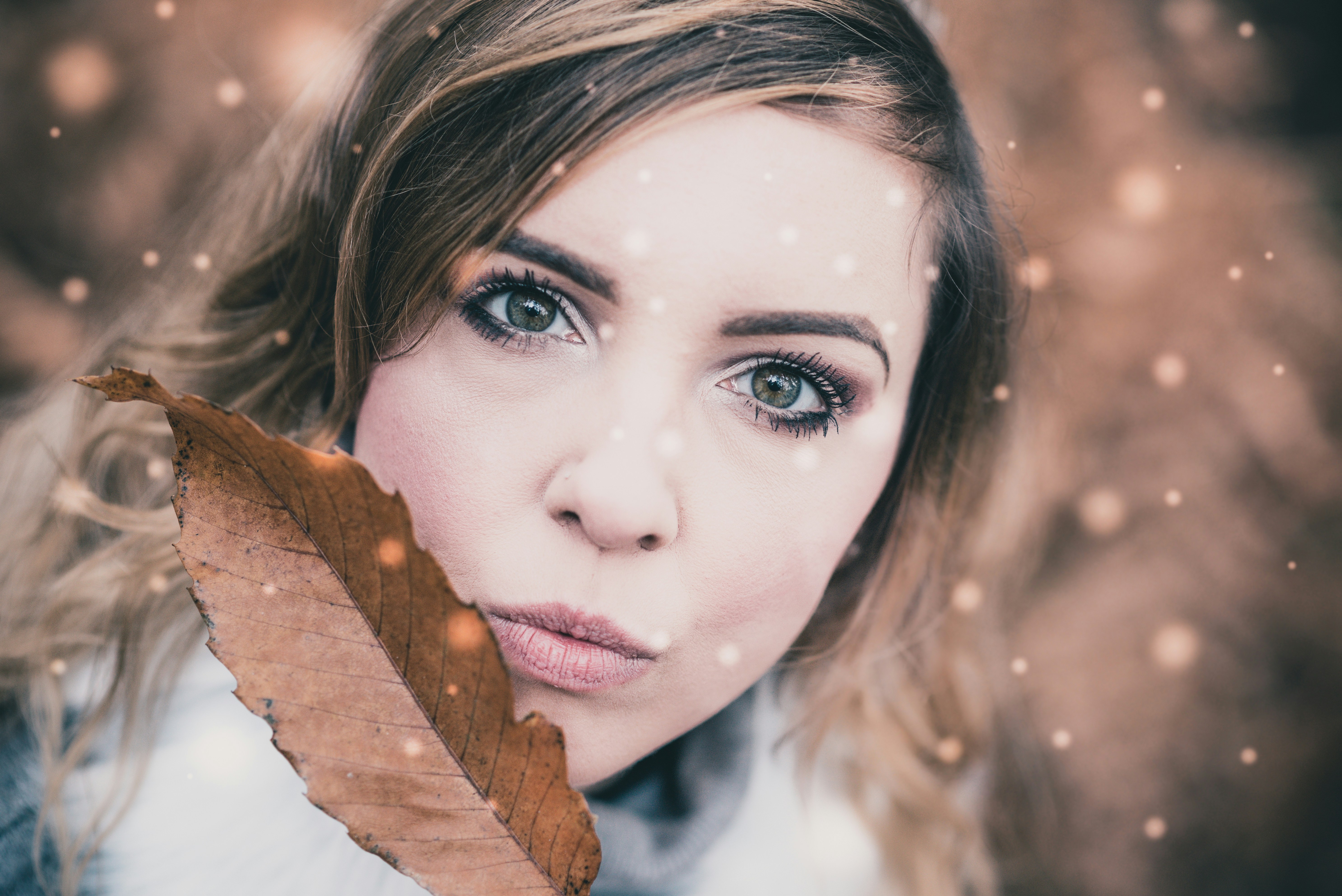 Woman holding a brown leaf with a softly blurred autumn background.