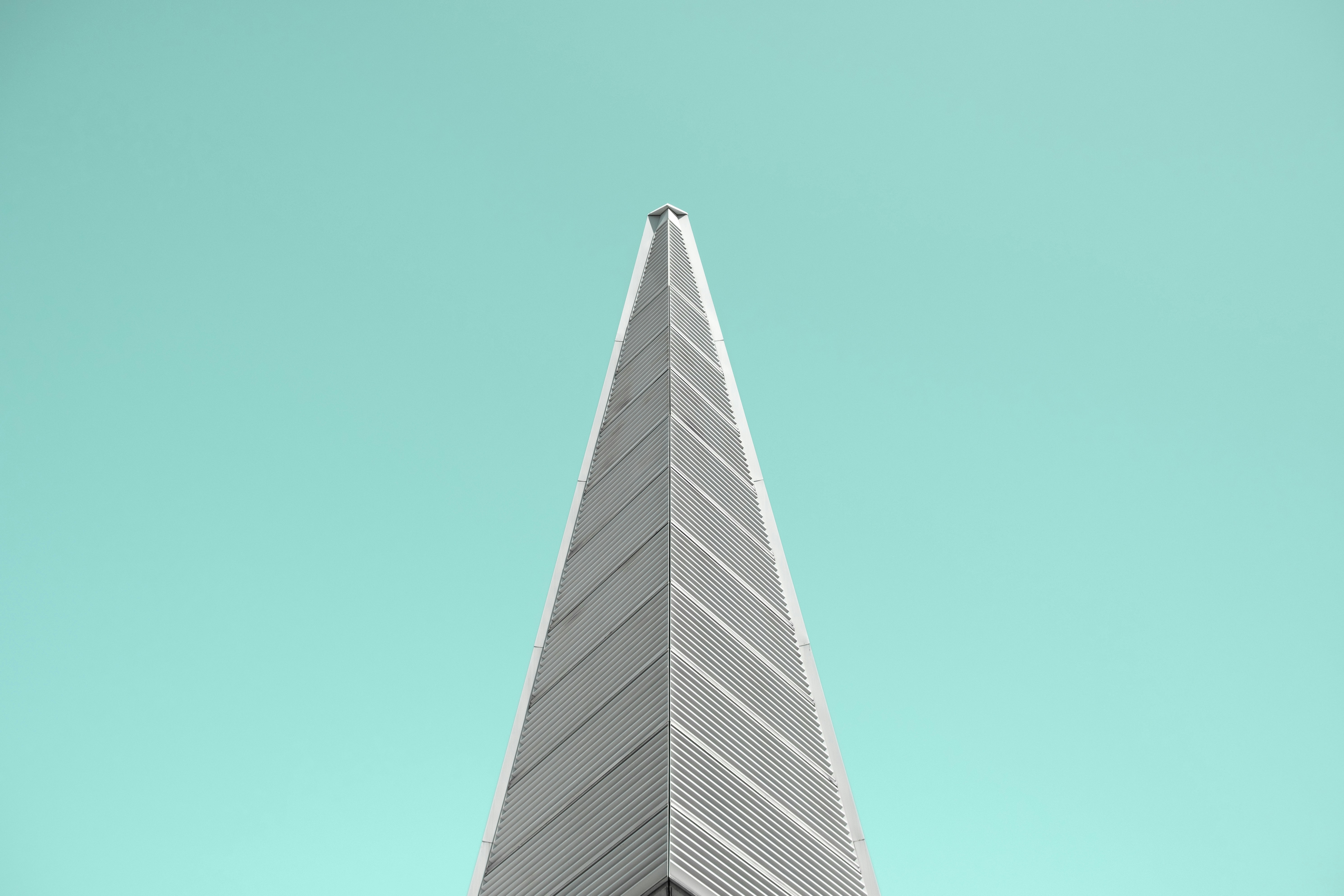 Tall architectural spire reaching towards a turquoise sky, showcasing clean lines and a minimalist design.