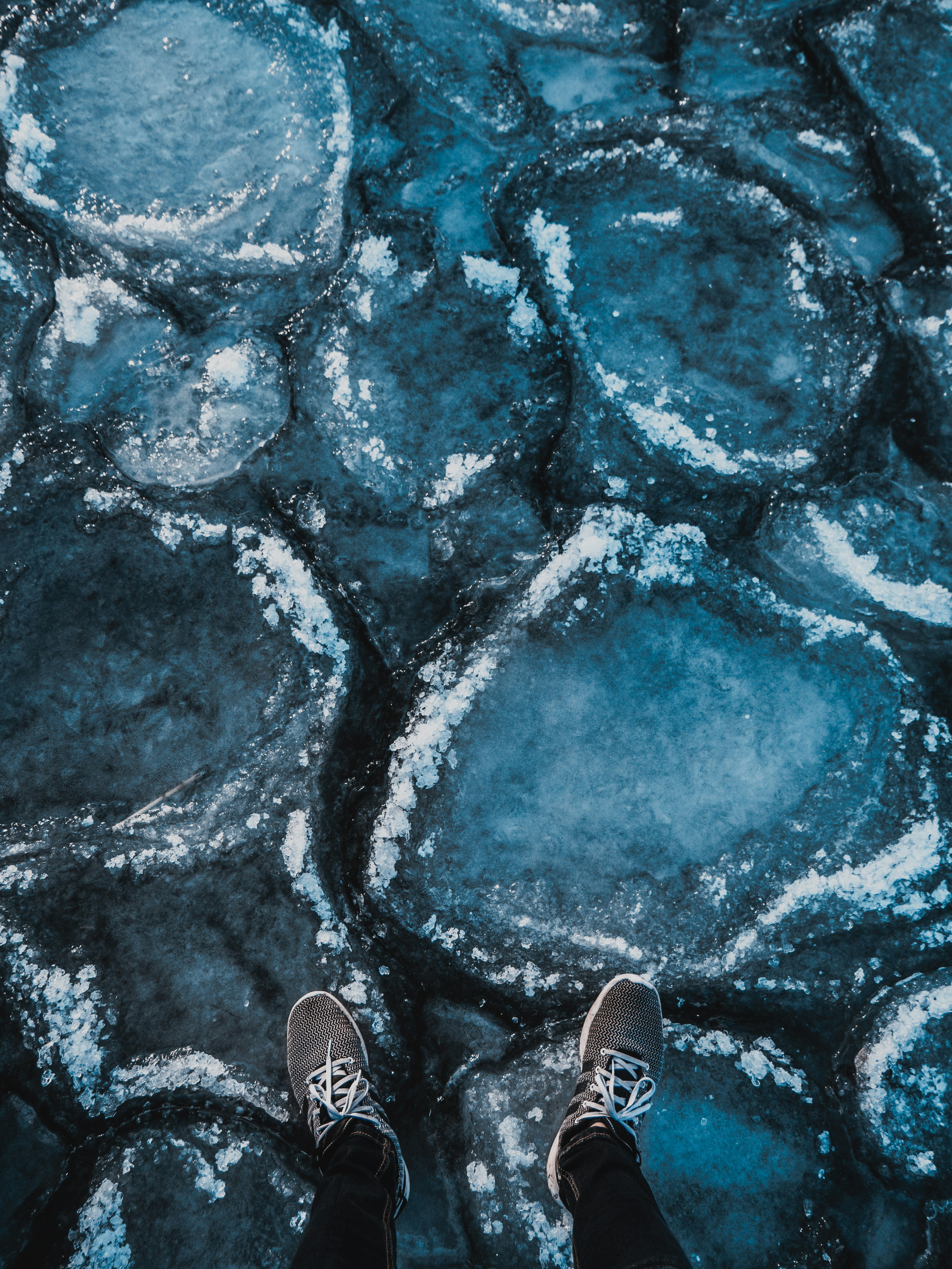 person in black and white sneakers standing on rocky shore