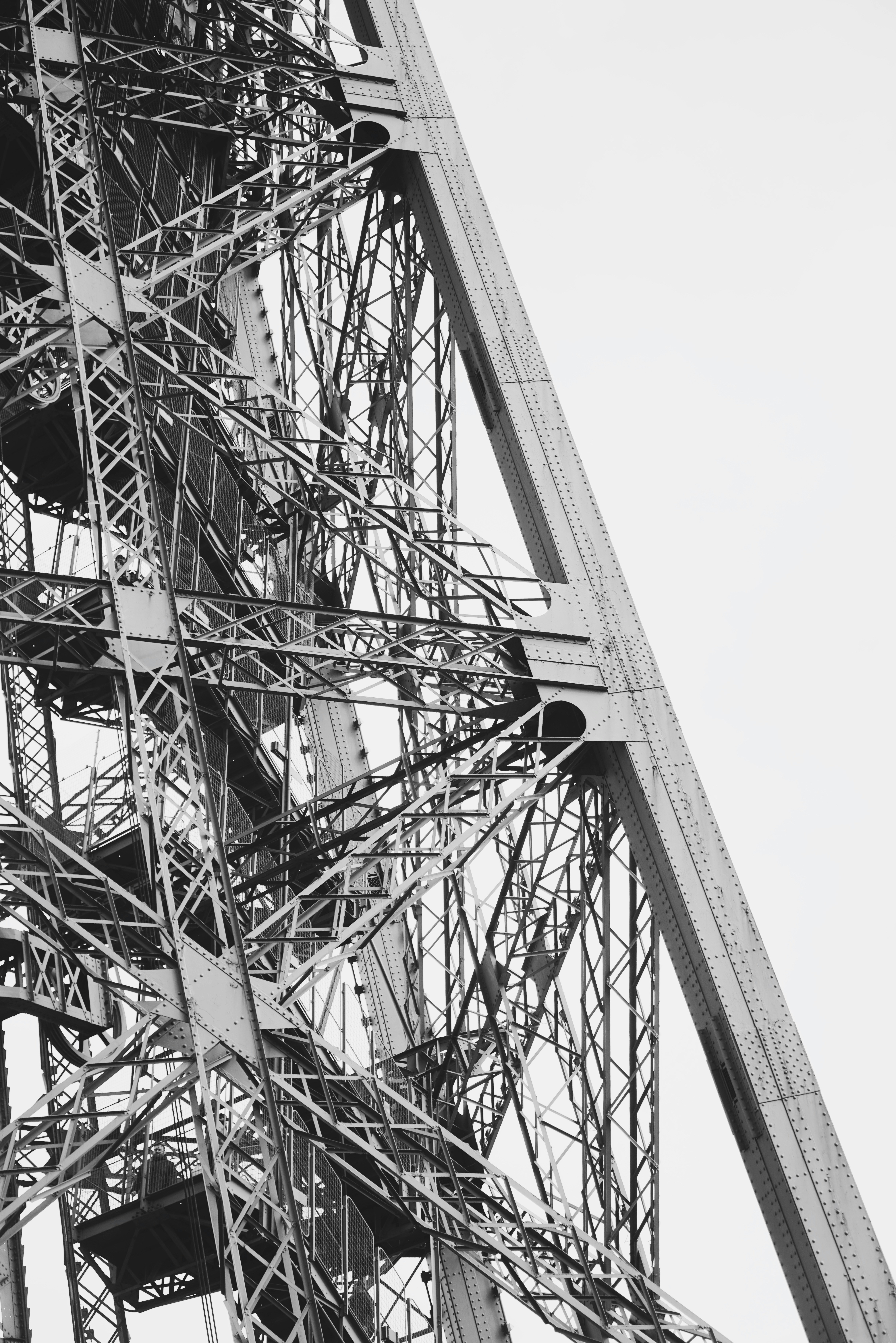 Close-up view of the intricate steel framework of a tower, showcasing its geometric patterns and structural design. The monochrome palette emphasizes the details and textures.