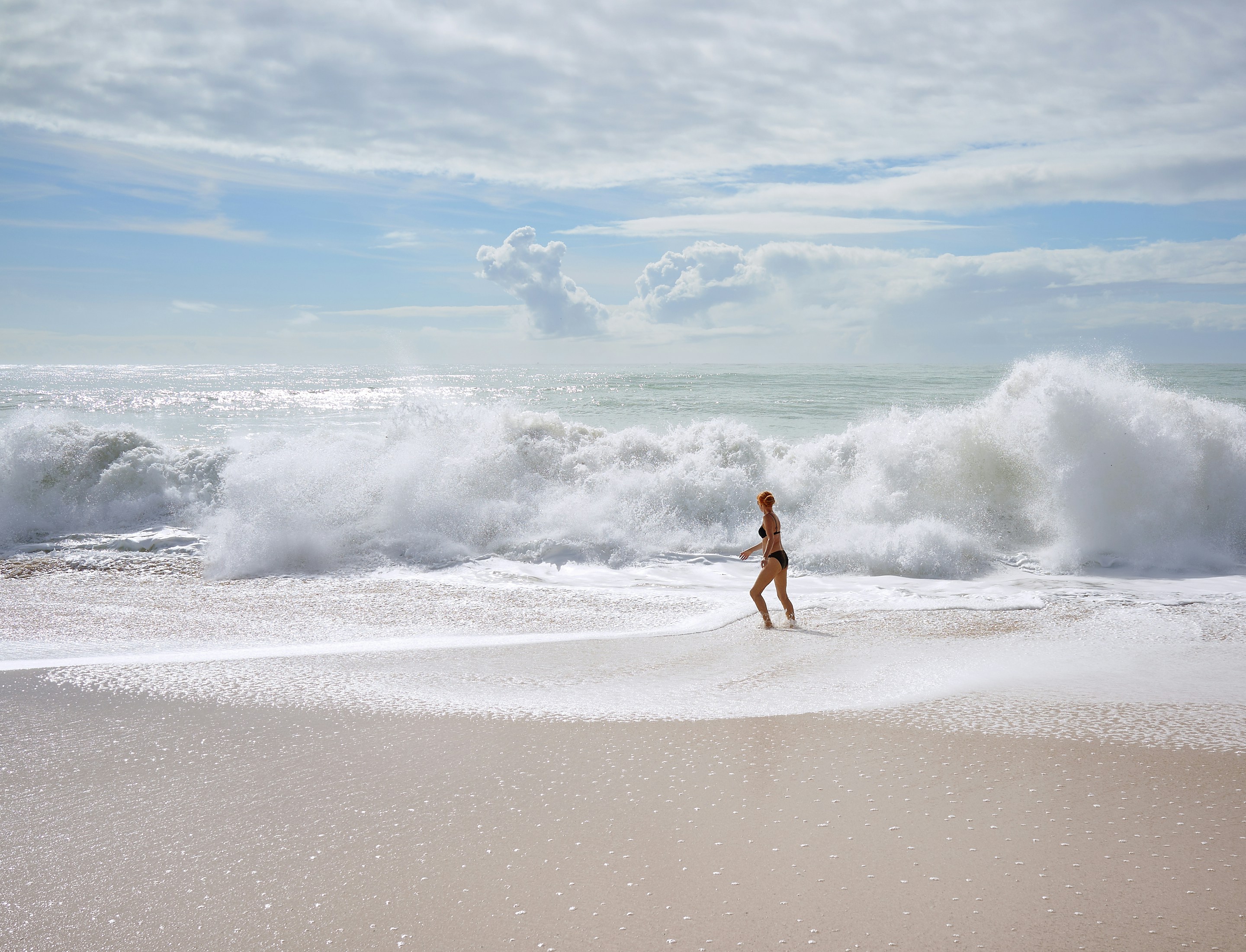 A solitary figure walks along the shoreline as powerful waves crash nearby, capturing the essence of tranquility amidst nature's energy.