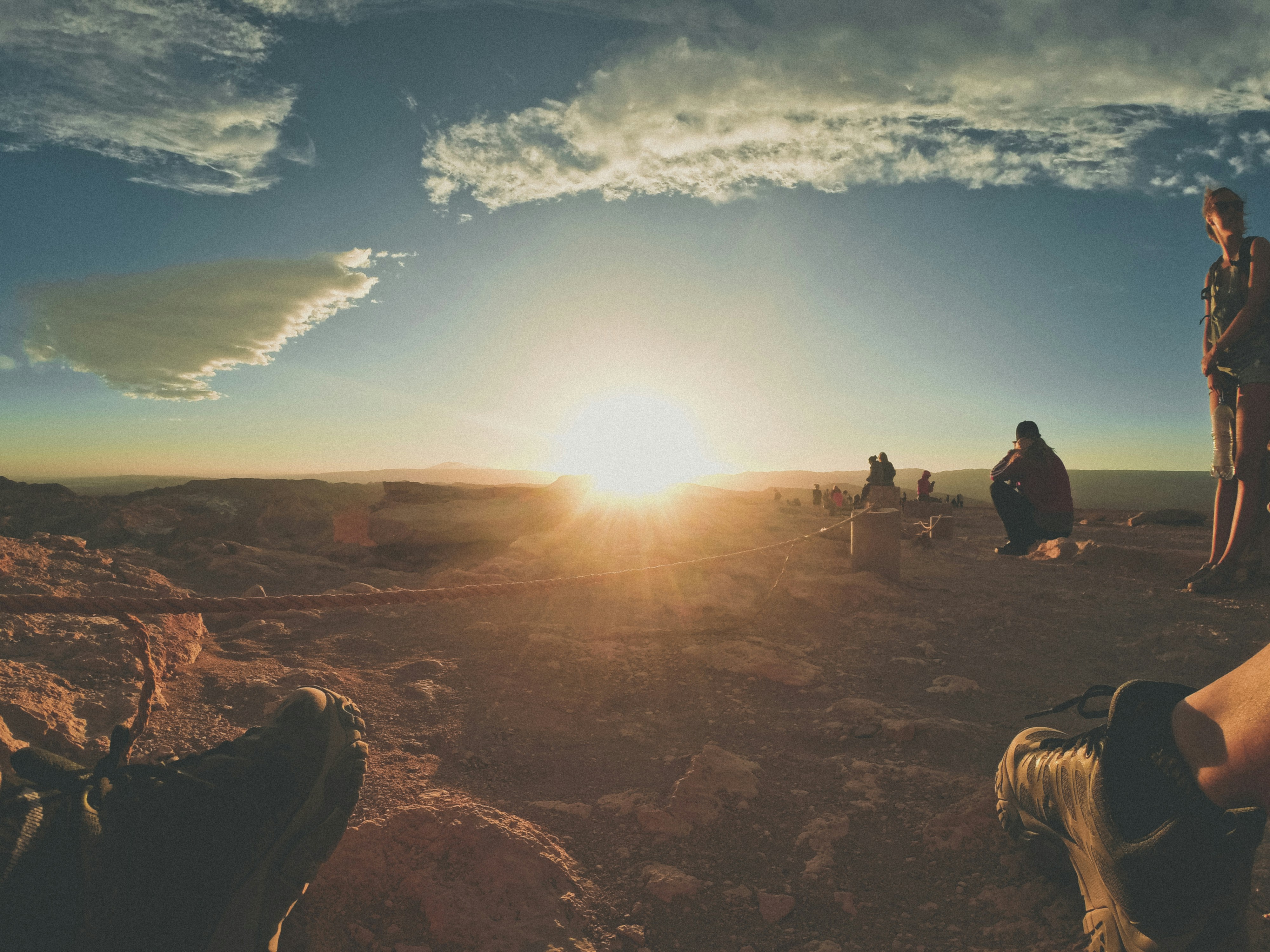 Silhouetted figures enjoying a sunset on rocky terrain, with a vibrant sky painted in warm hues. The scene captures a moment of connection with nature.