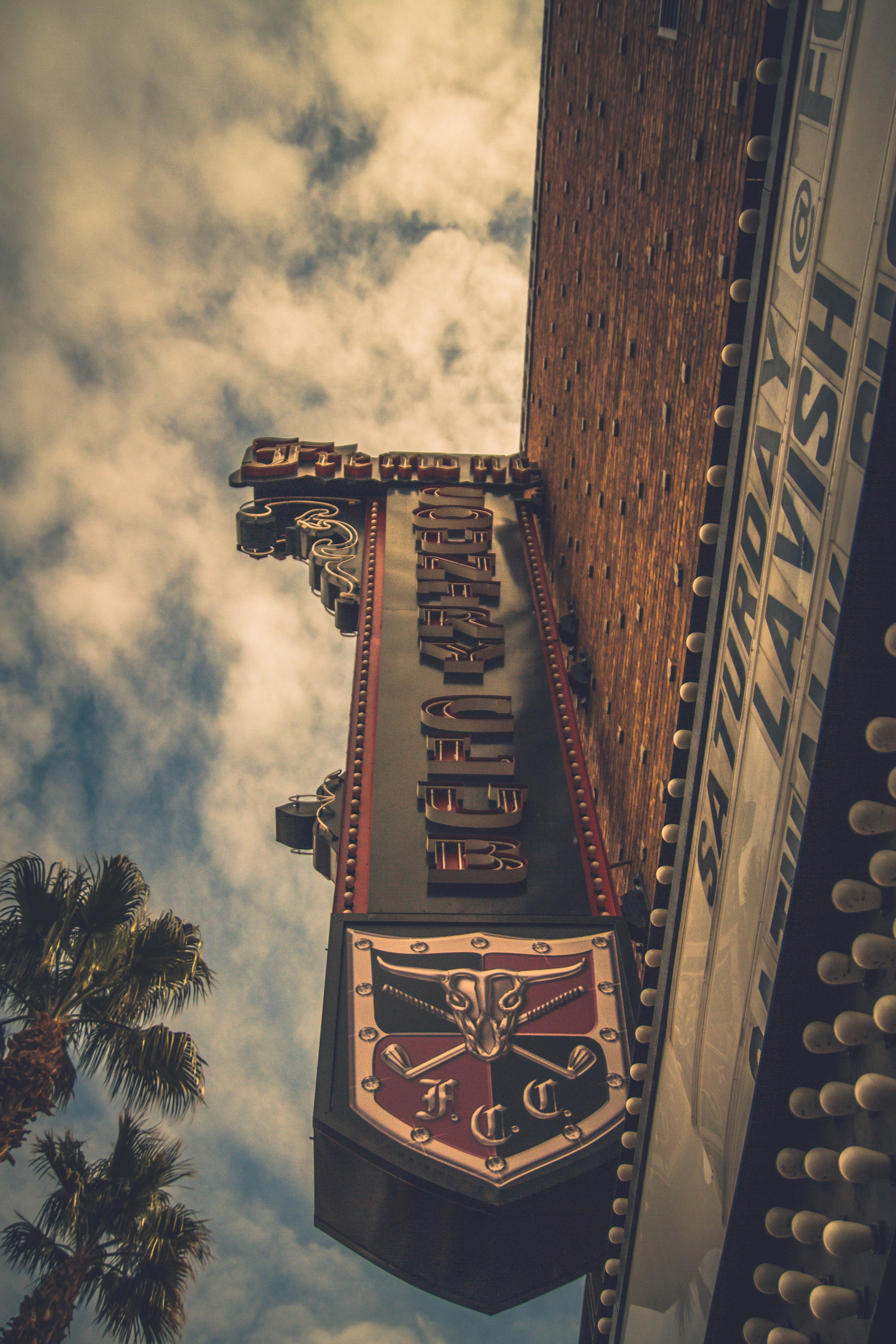 Historic theater marquee showcasing intricate design and bold lettering against a cloudy sky, flanked by palm trees.
