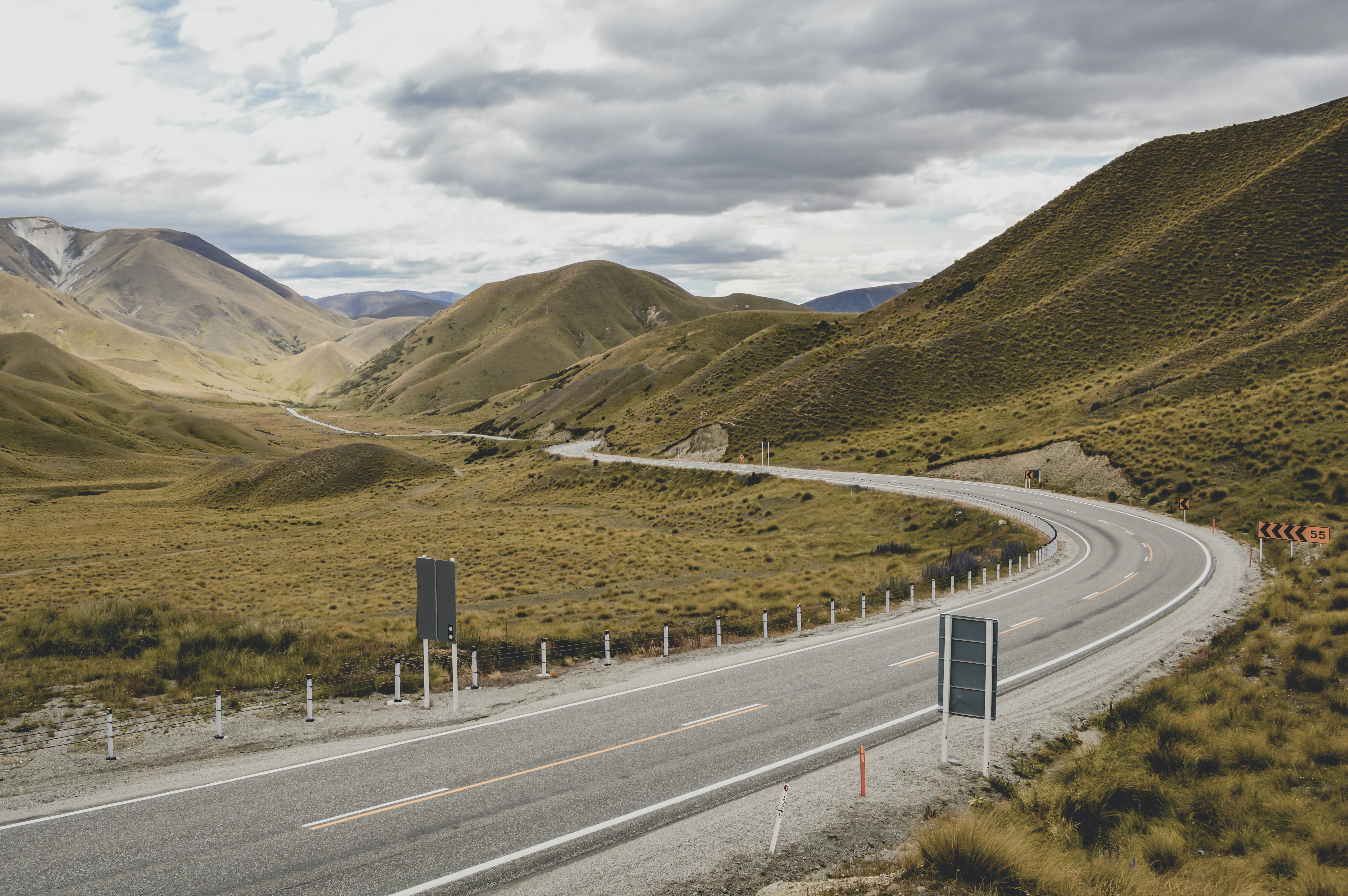 Winding road curves through grassy hills under a cloudy sky.