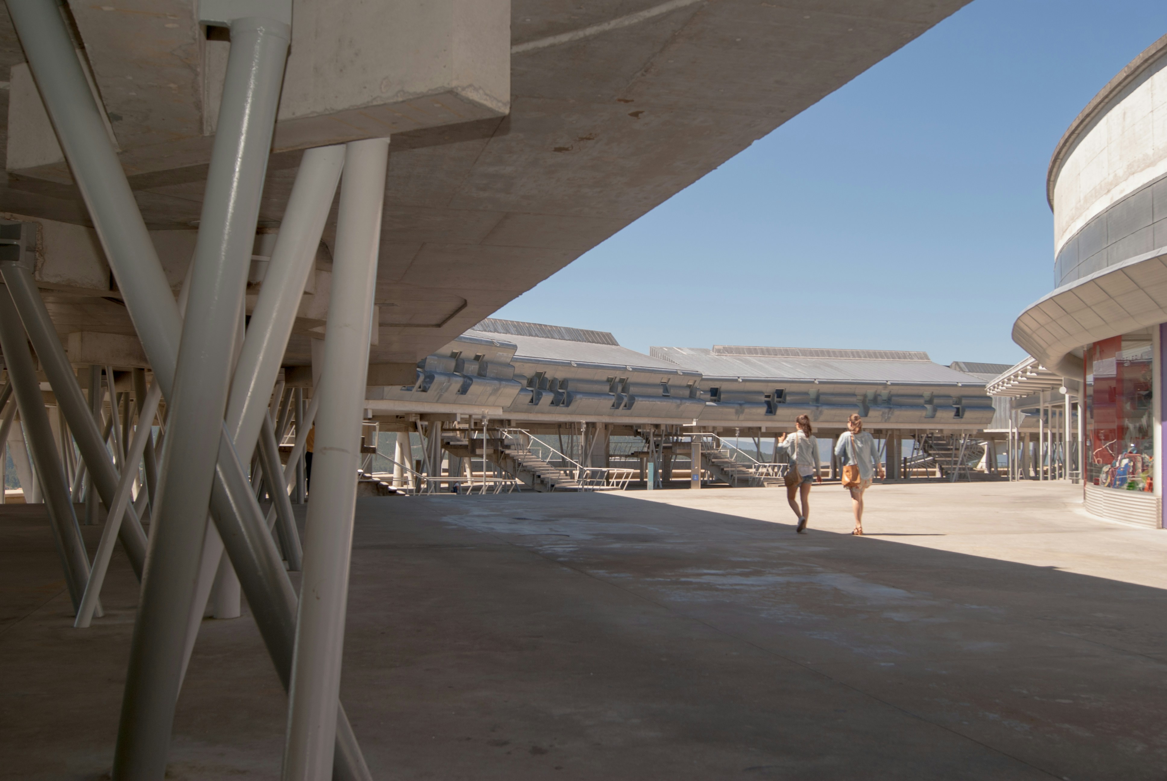 Modern architectural structures with angled beams and curved walkways under a clear blue sky.