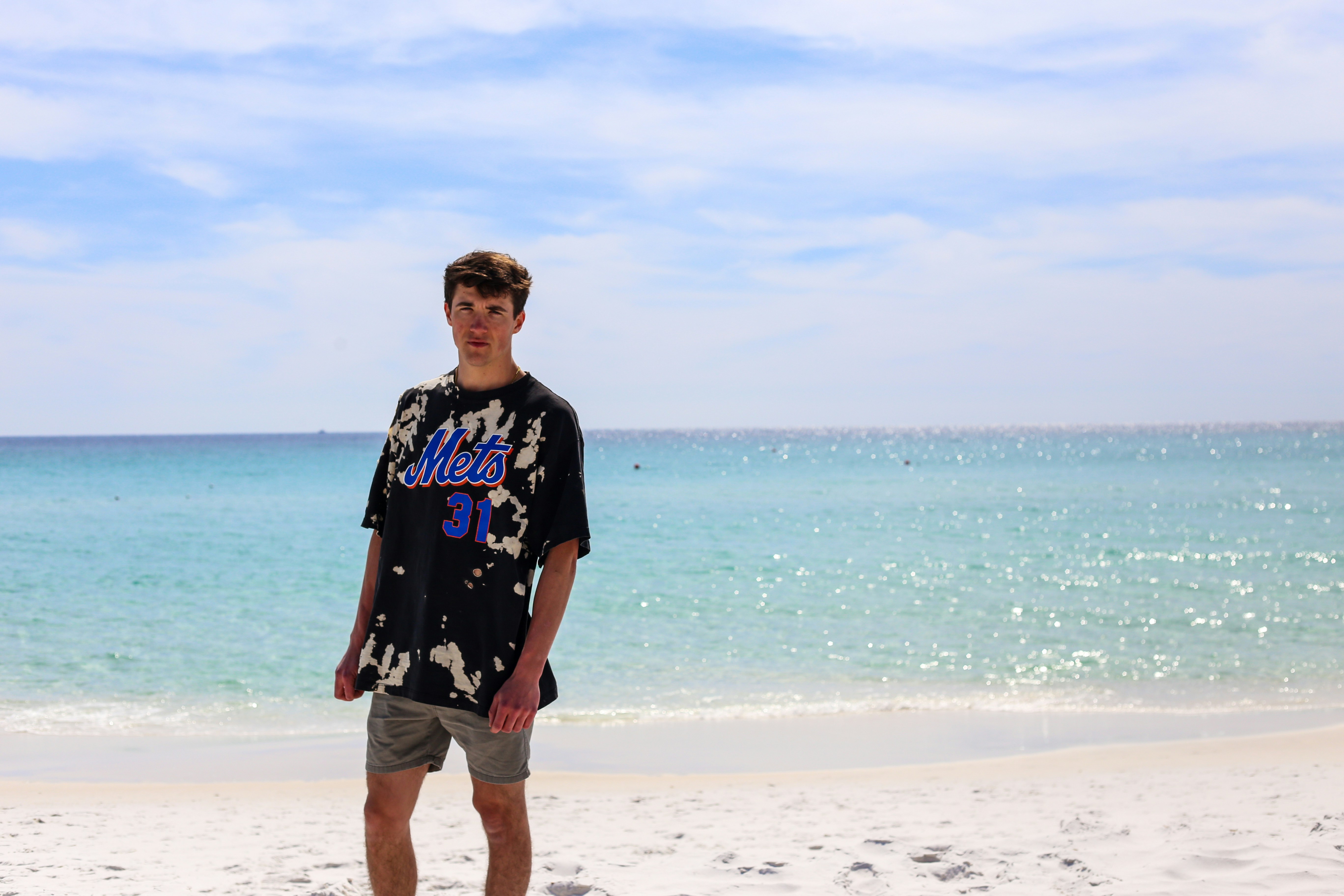 Person standing on a white sandy beach with turquoise ocean and blue sky in the background.