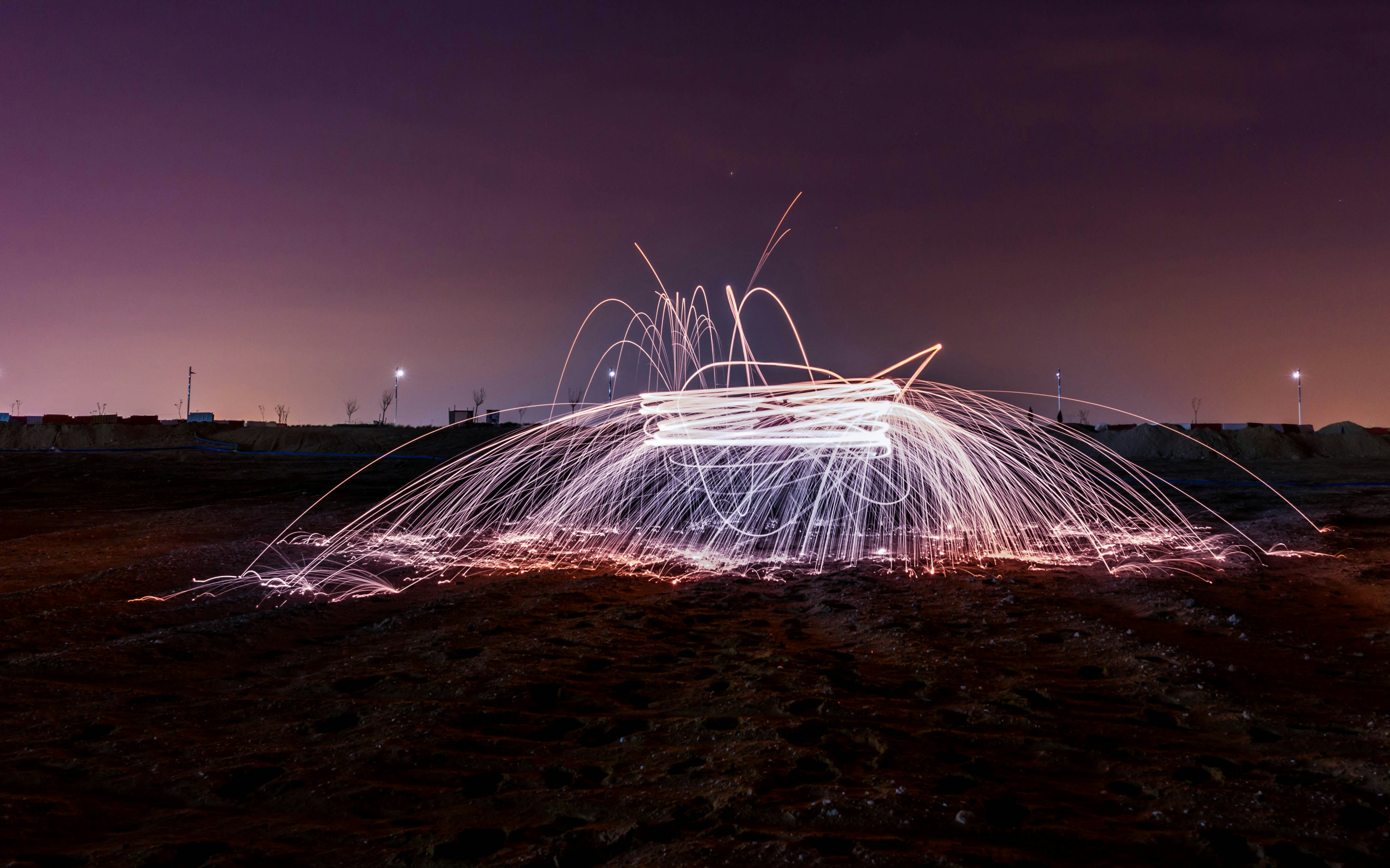 Long exposure of steel wool spinning, creating arcs of light against a dusky sky.