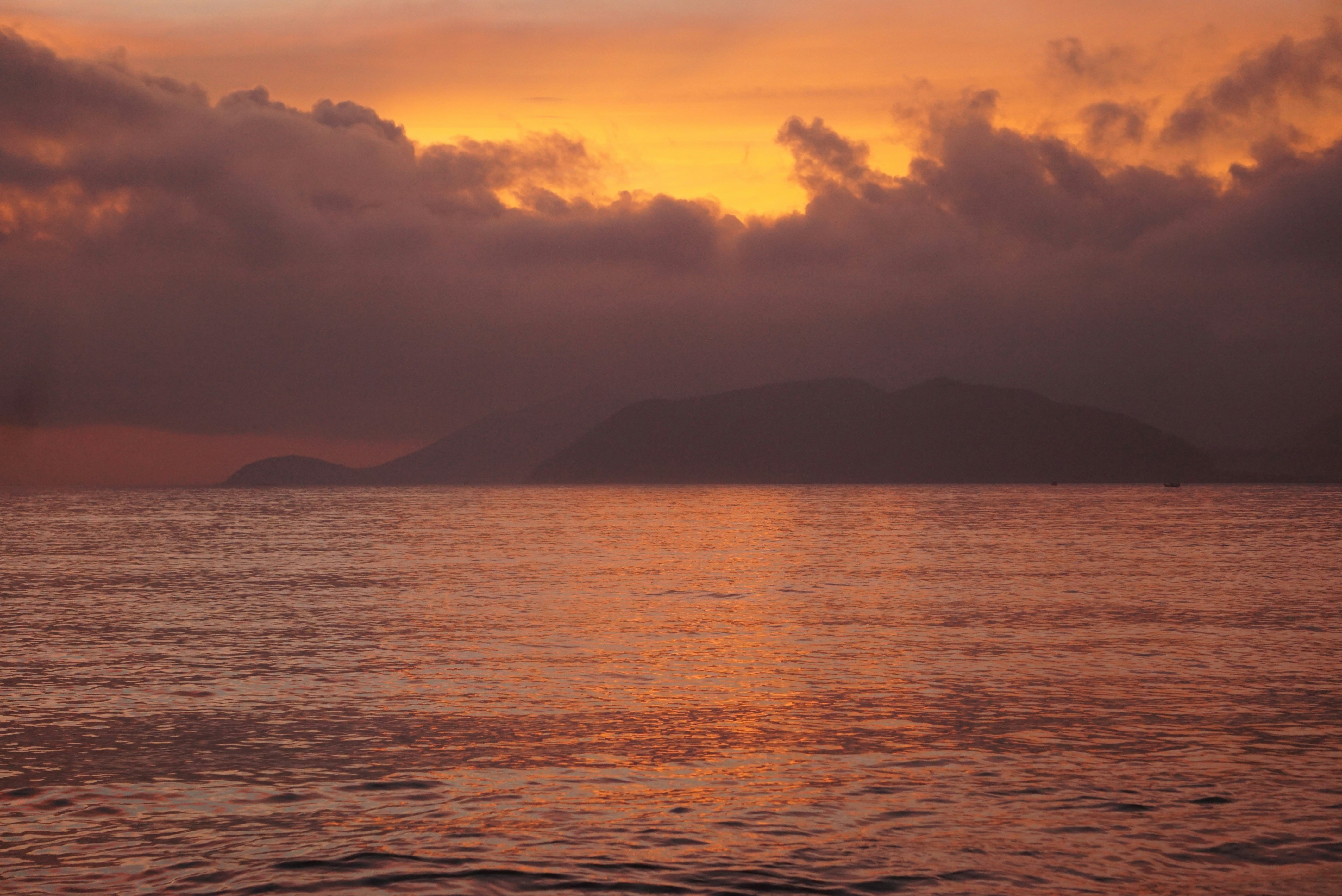Golden hues reflect off the calm sea as clouds gather in the twilight sky, hinting at the approaching night.