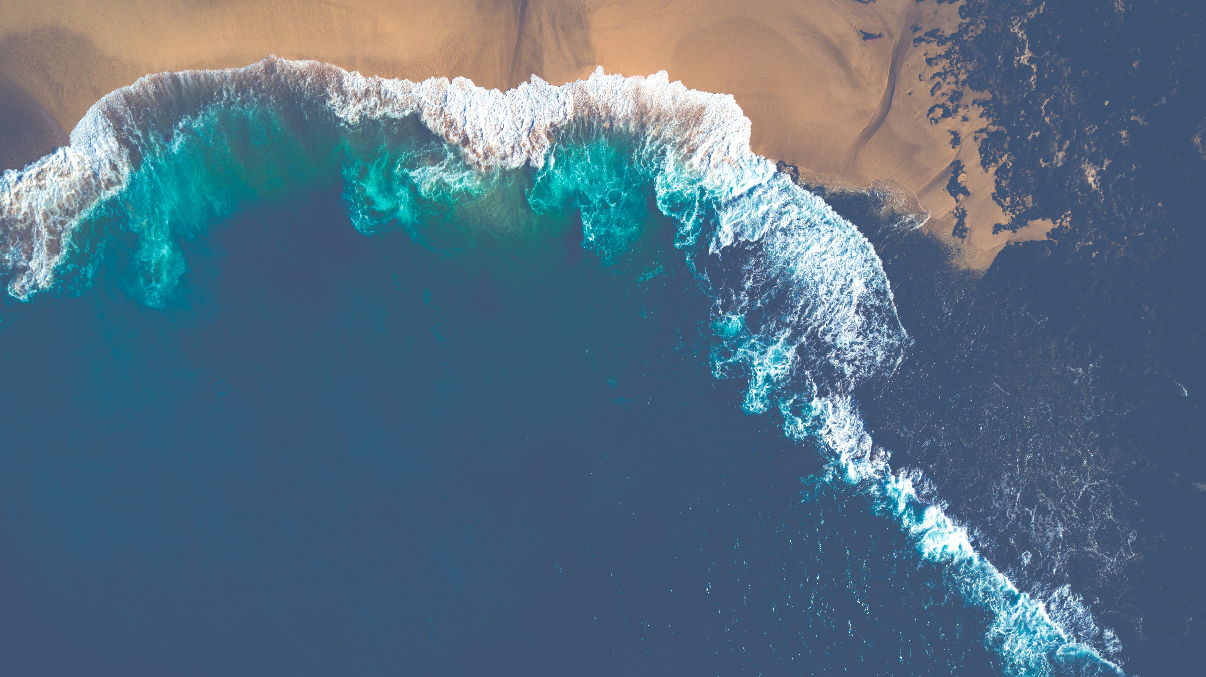 Aerial view of turquoise waves crashing onto a sandy beach, showcasing the dynamic interplay between land and sea.