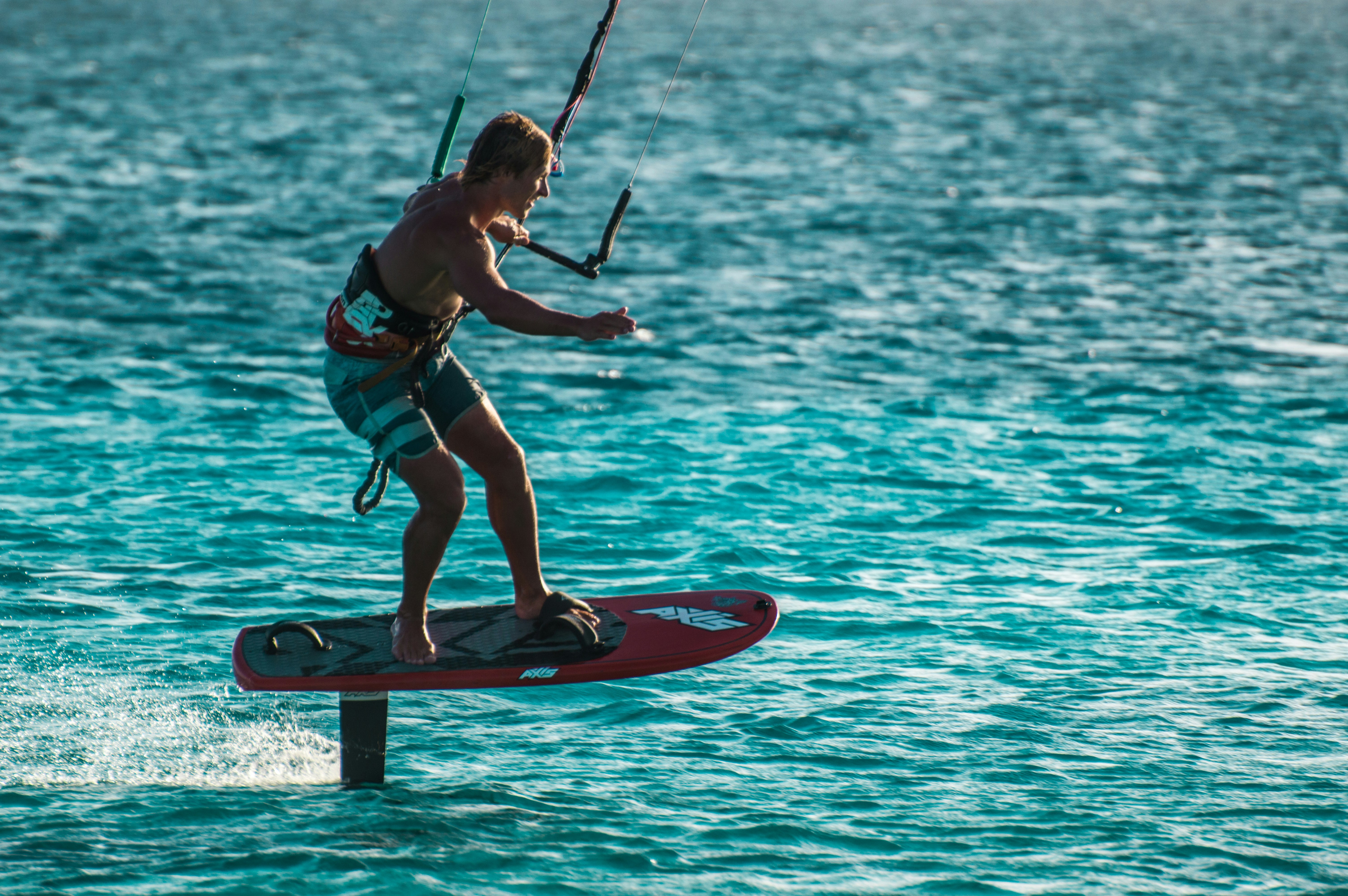 Kiteboarder performing a maneuver above shimmering turquoise waters. The dynamic motion captures the thrill of water sports.