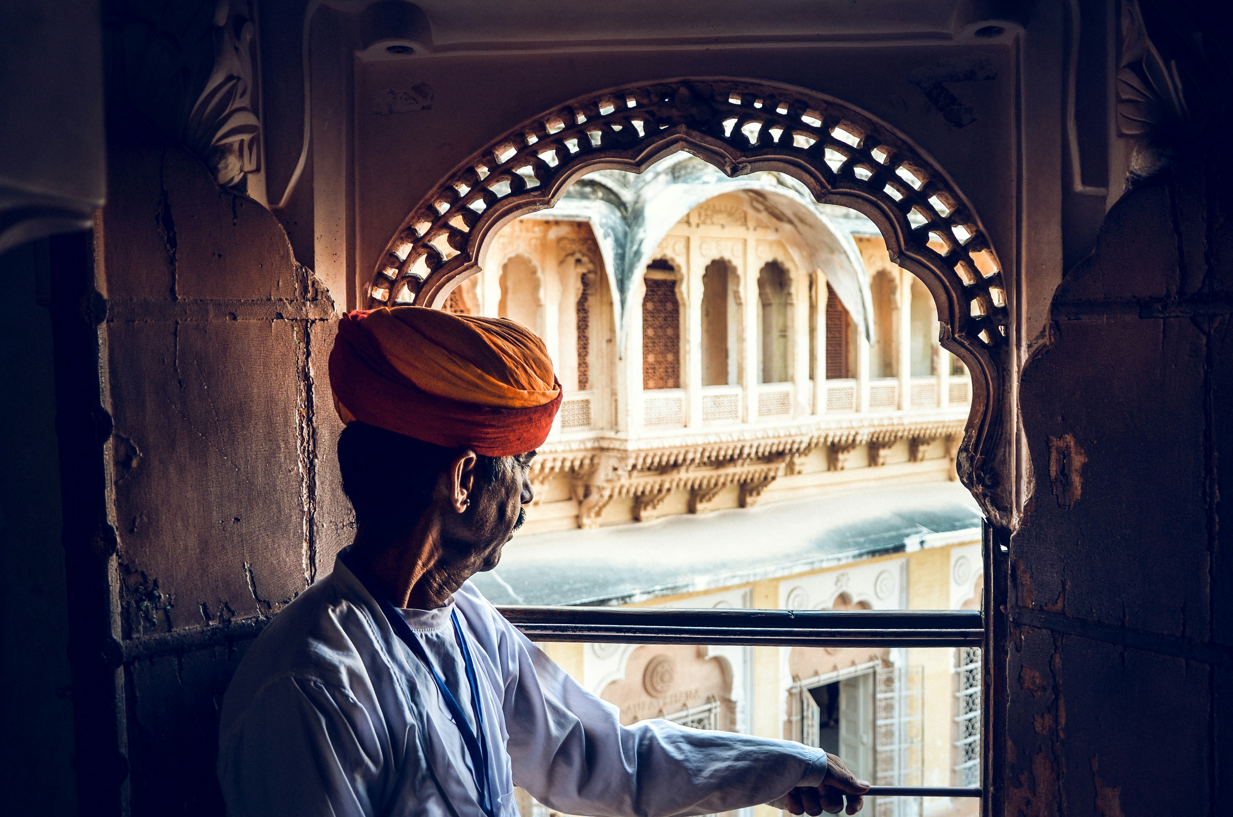 Person in traditional attire gazing through an ornate arch at historic architecture.