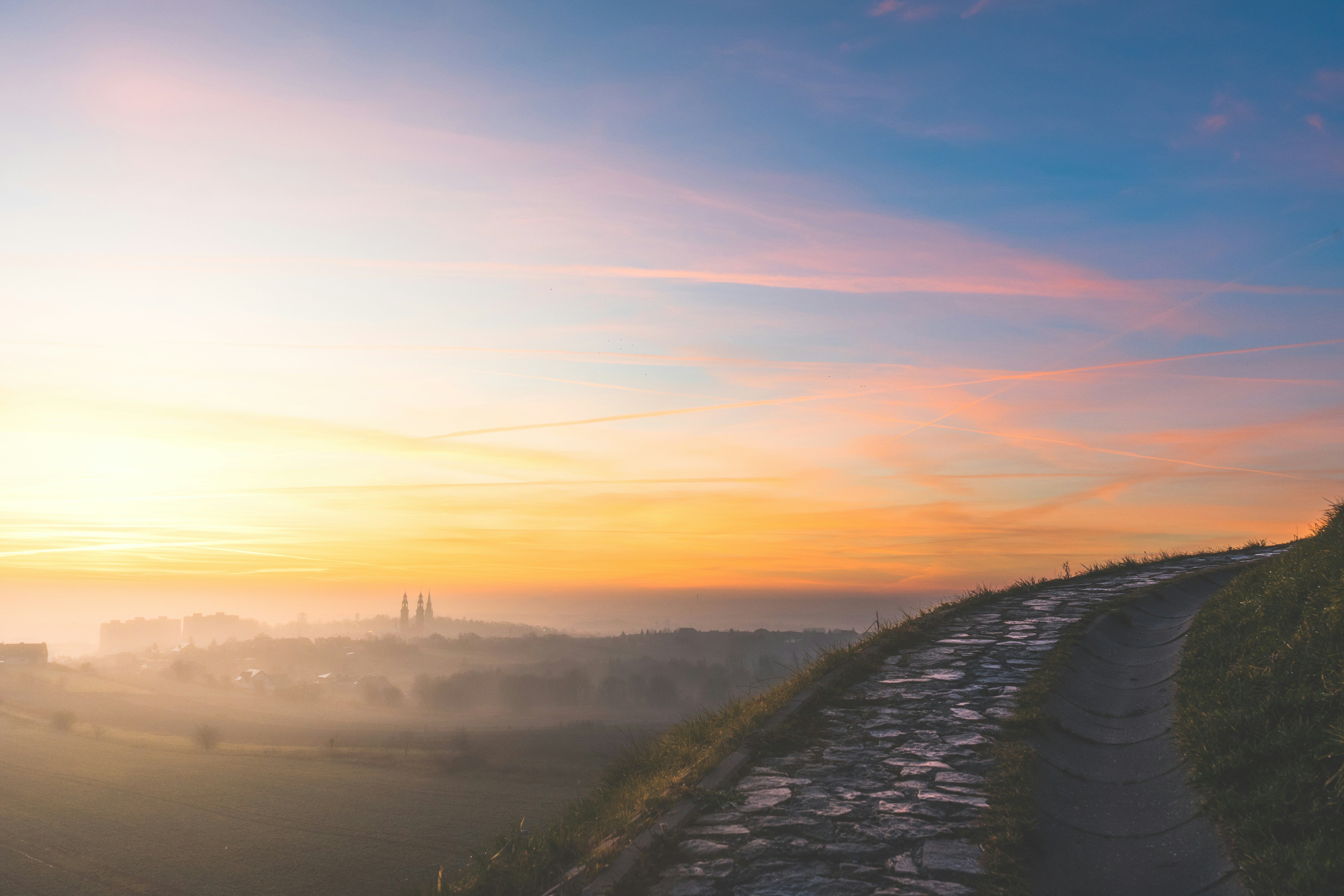 Foggy sunrise over a rural landscape with a stone path leading into the distance.