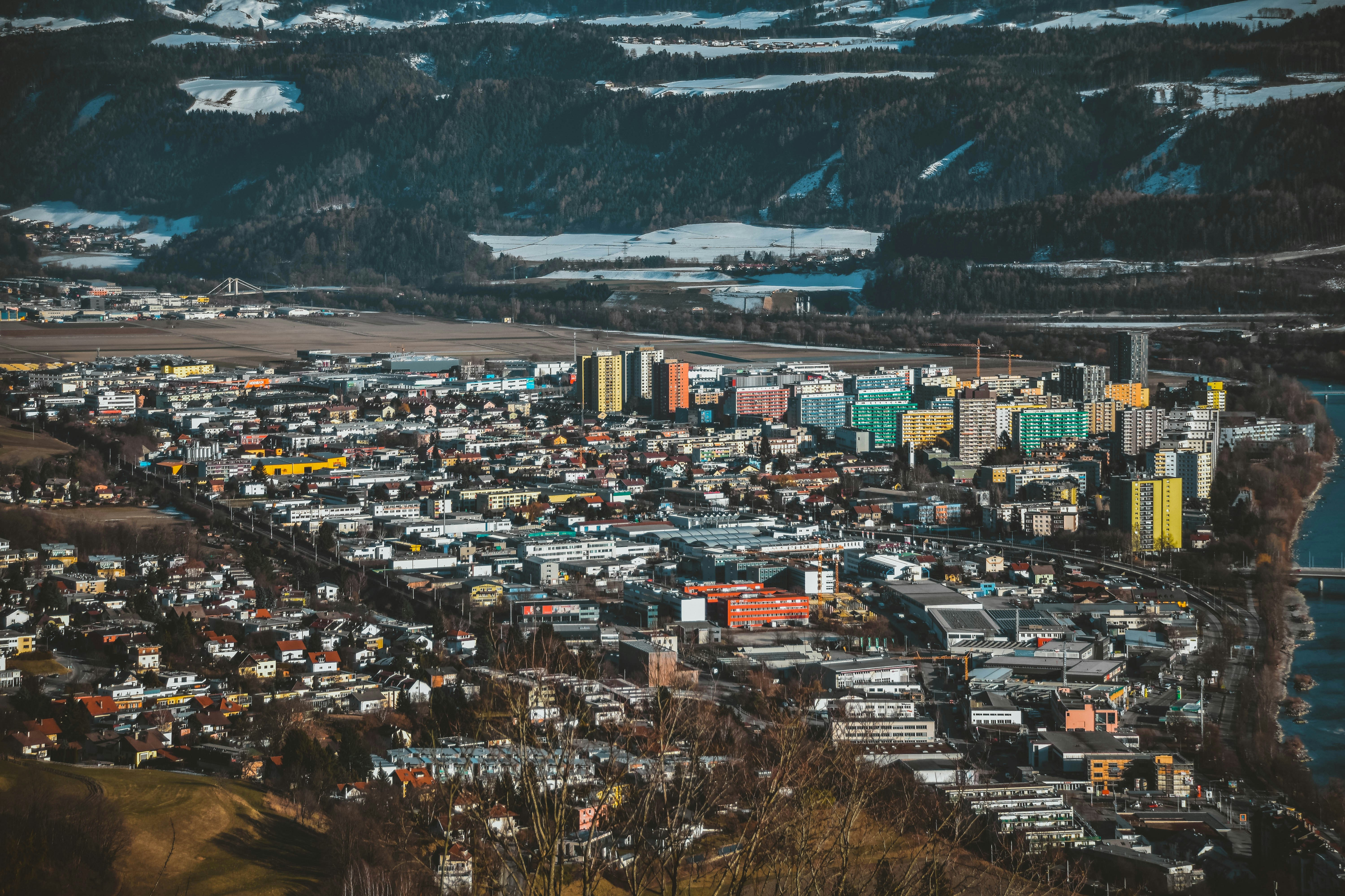 Aerial view of a vibrant cityscape, showcasing a blend of residential and commercial buildings against a backdrop of snow-capped mountains.