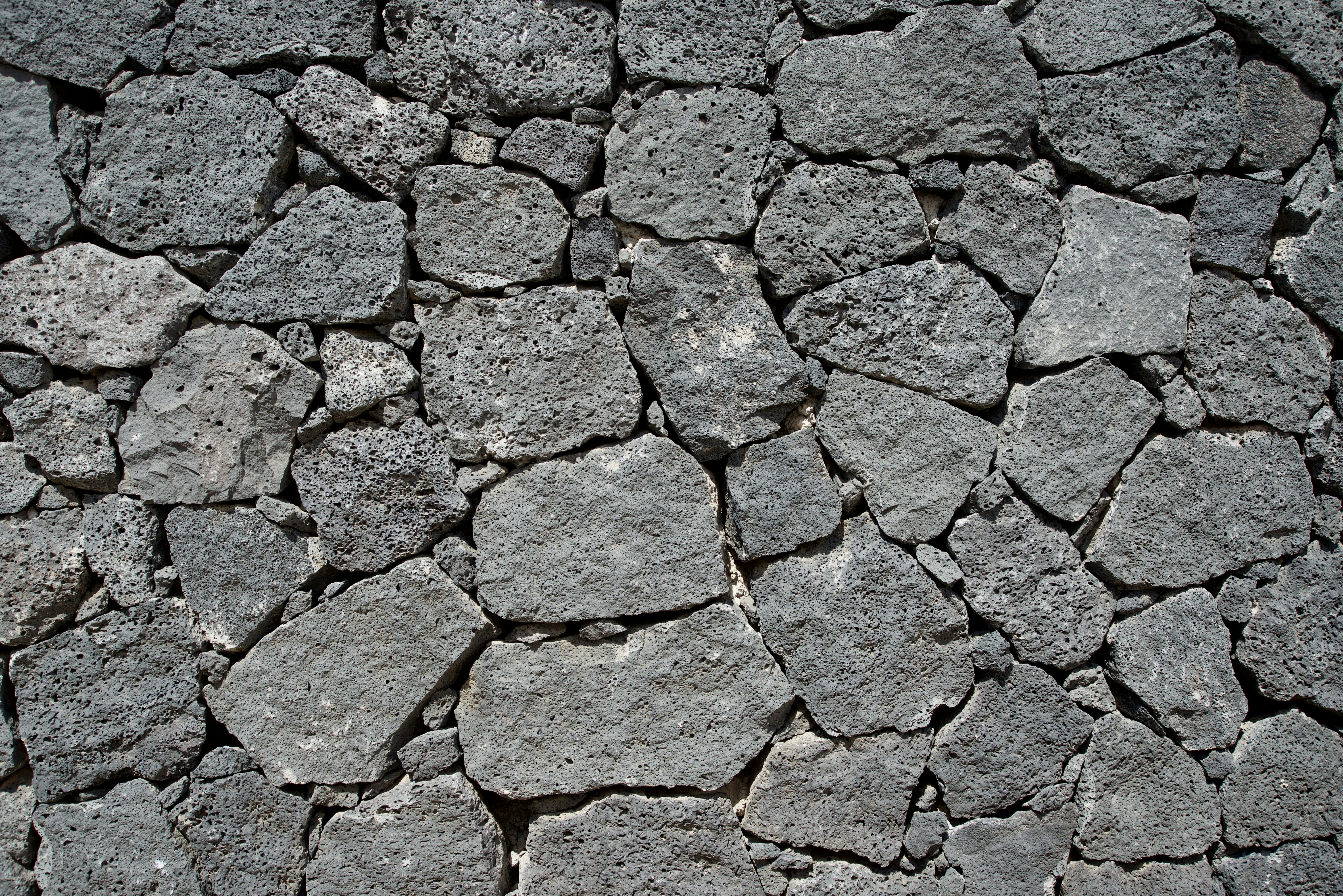 Close-up of a rugged stone wall composed of irregularly shaped volcanic rocks, showcasing a natural and rustic texture. Ideal for architectural backgrounds and design elements. © Gavin Allanwood 2024 | photo of gray pavement