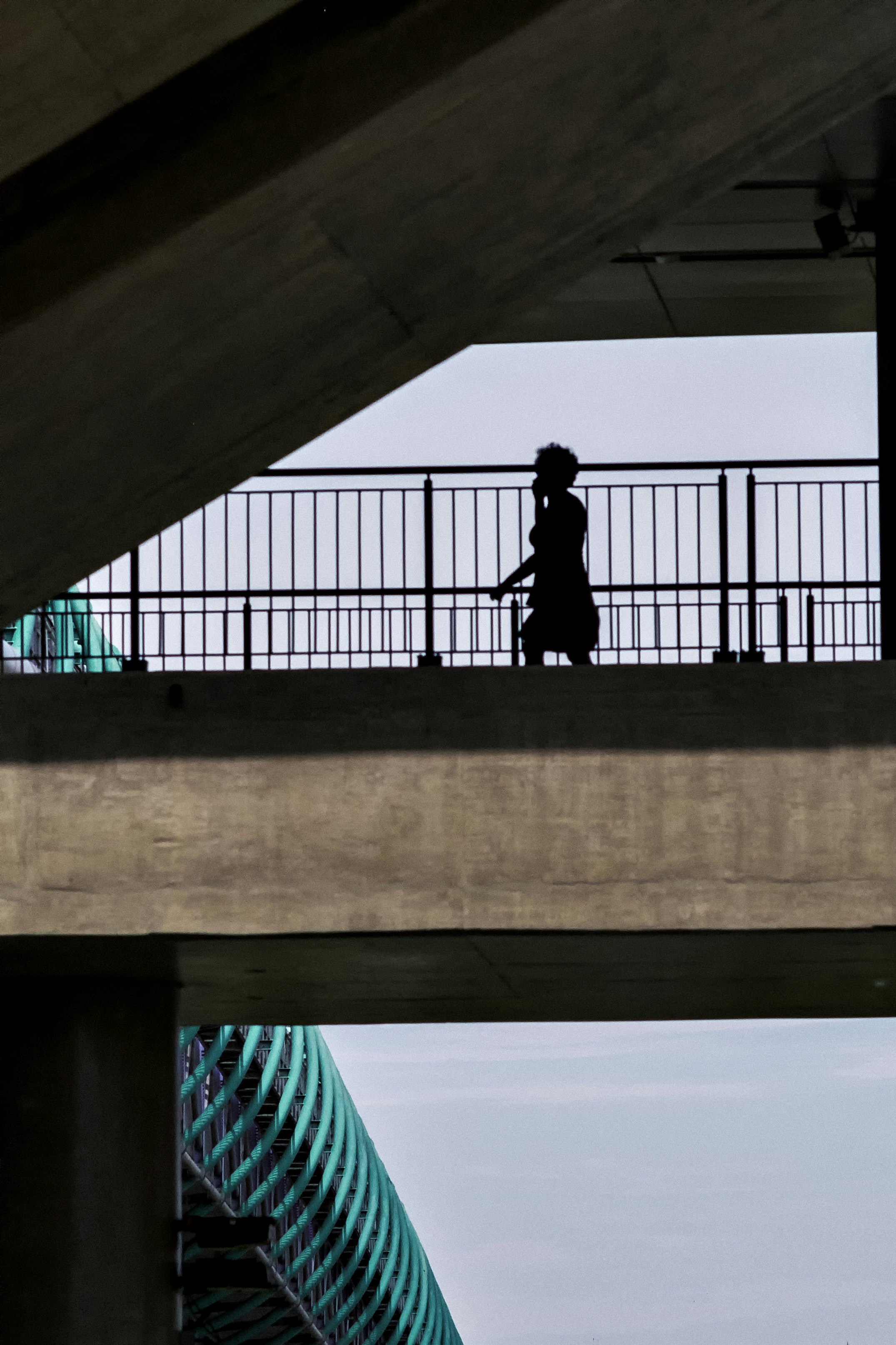 Solitary silhouette on a concrete overpass beneath teal ribbing