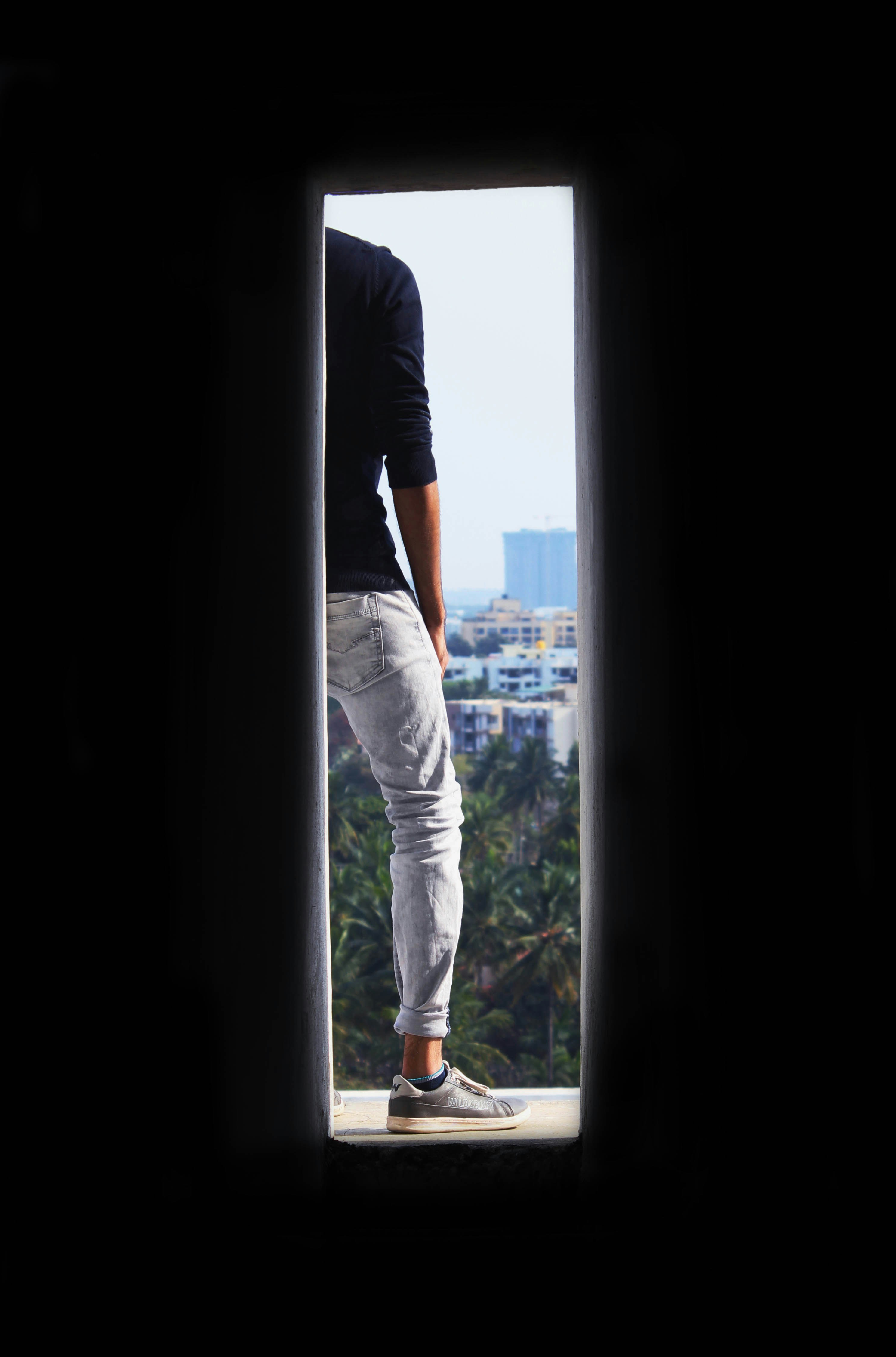 Silhouette of a person standing in a narrow opening, overlooking a vibrant cityscape with palm trees in the foreground.