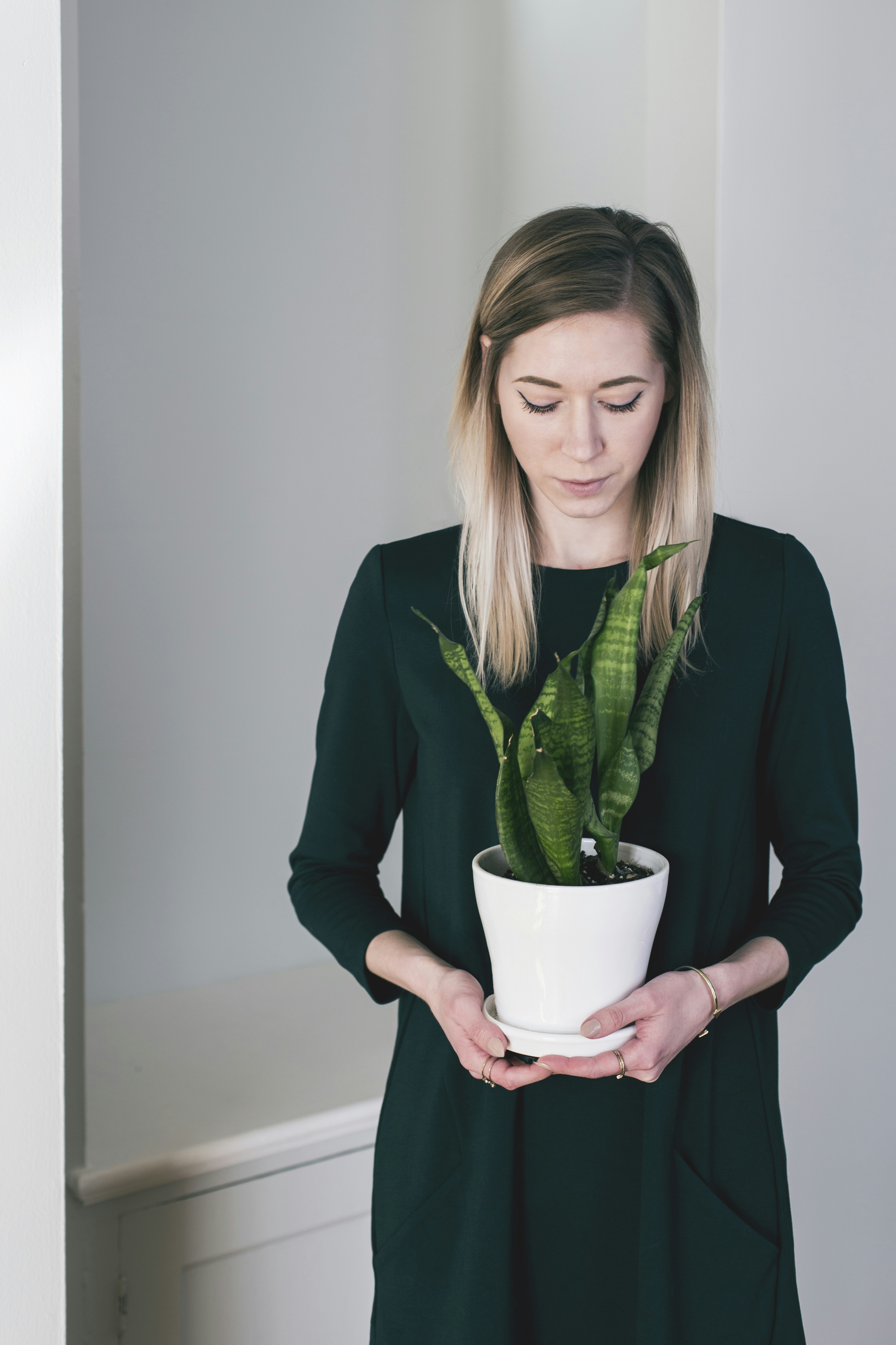 Woman in dark green attire gently cradles a potted snake plant, embodying a serene moment of connection with nature.