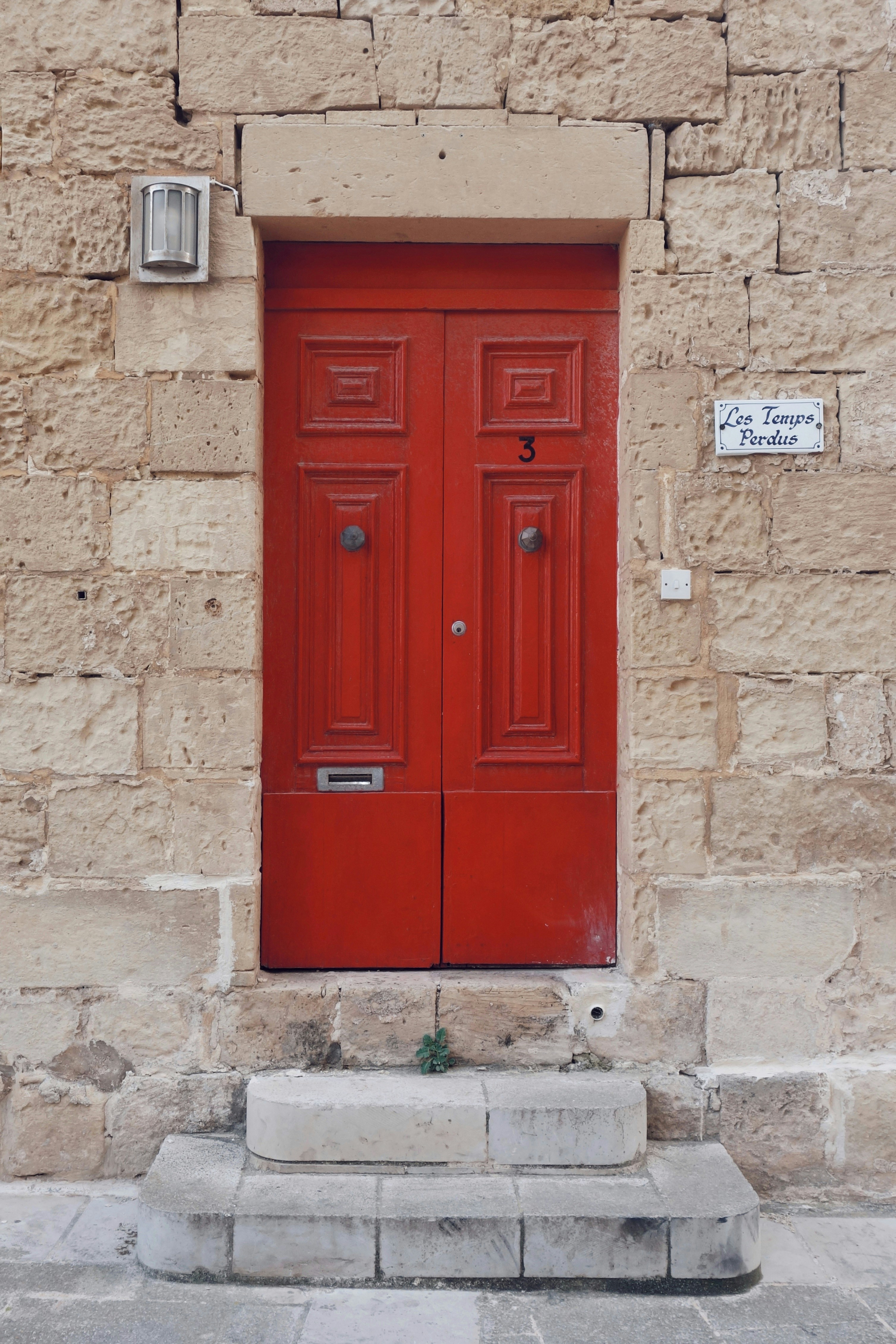 Vibrant red door framed by weathered limestone, with a stone step and a small plaque nearby.