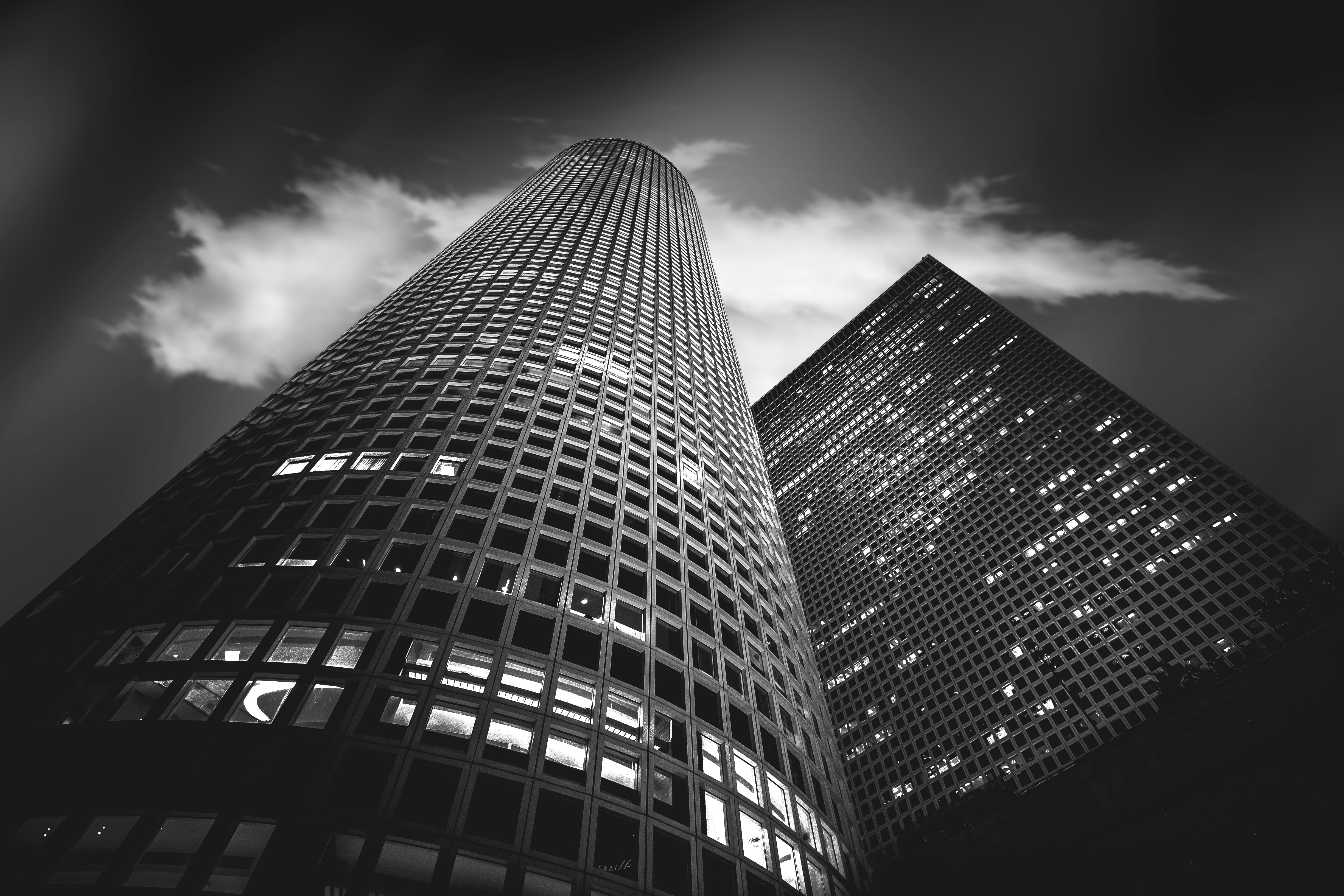 Black and white low-angle view of two modern skyscrapers with dramatic cloud above.