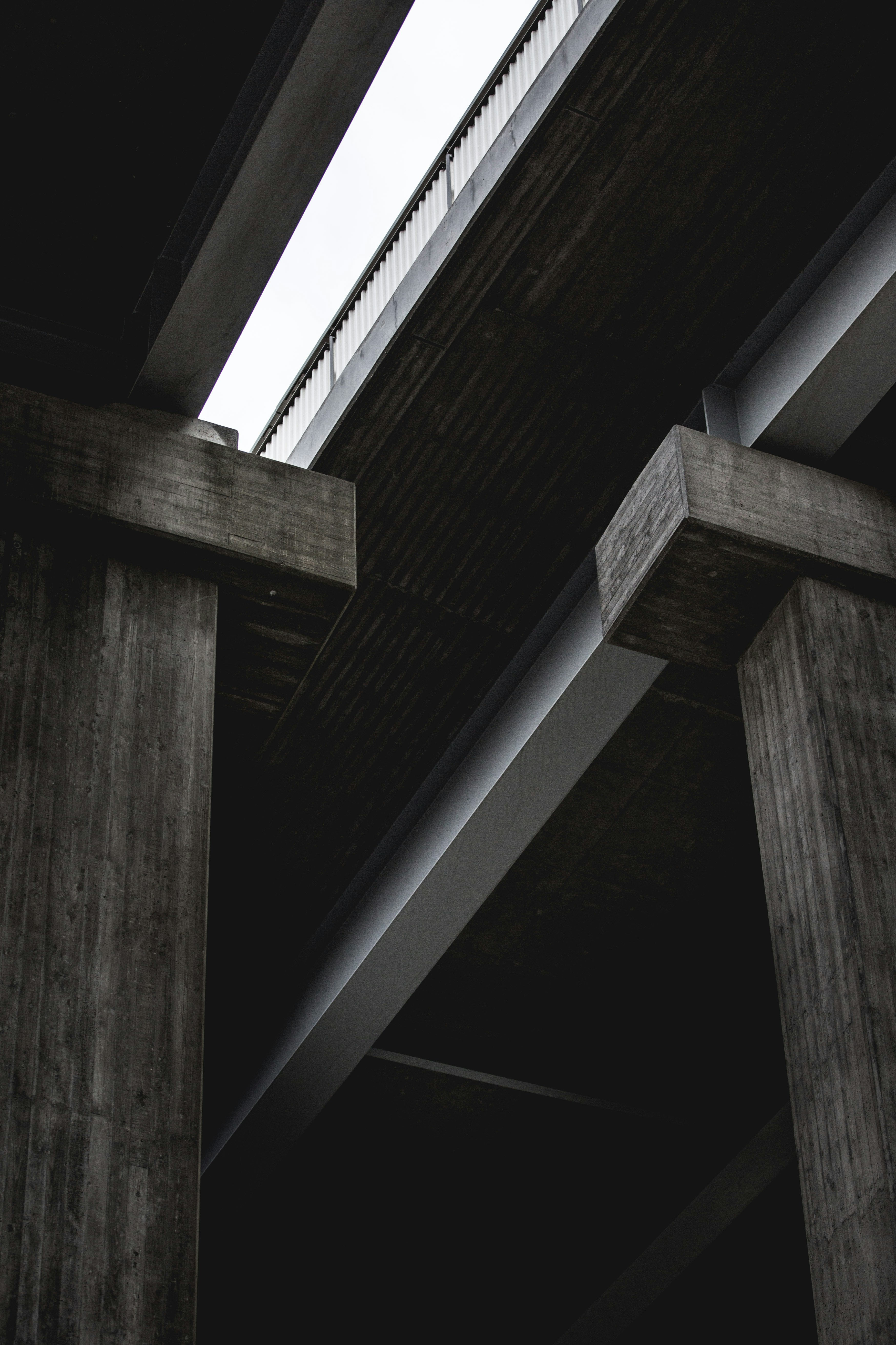 Abstract view of concrete pillars and beams under a bridge, showcasing geometric lines and contrasting shadows.